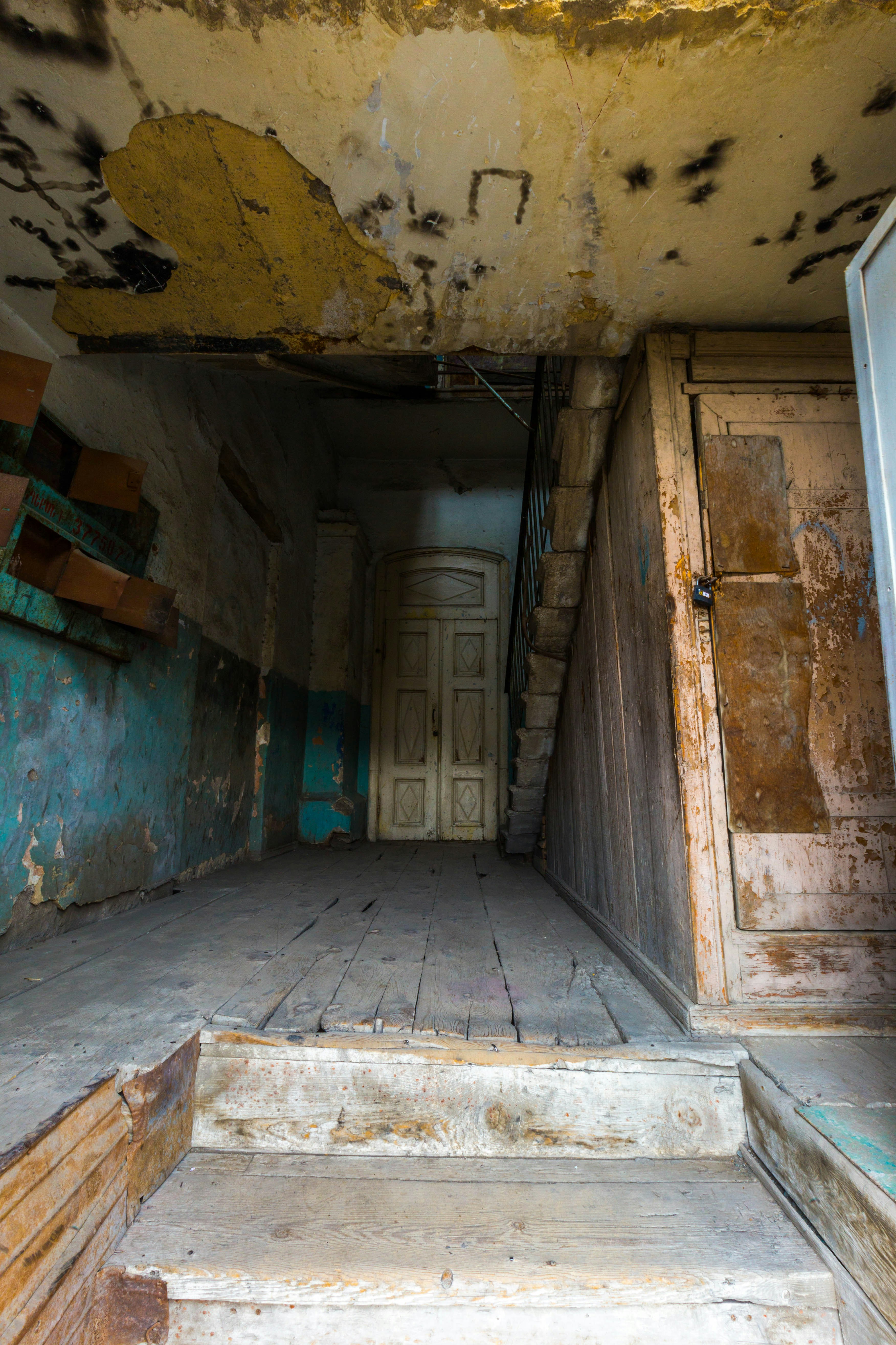 Dilapidated entrance with worn wooden stairs leading to a faded door in an old building.