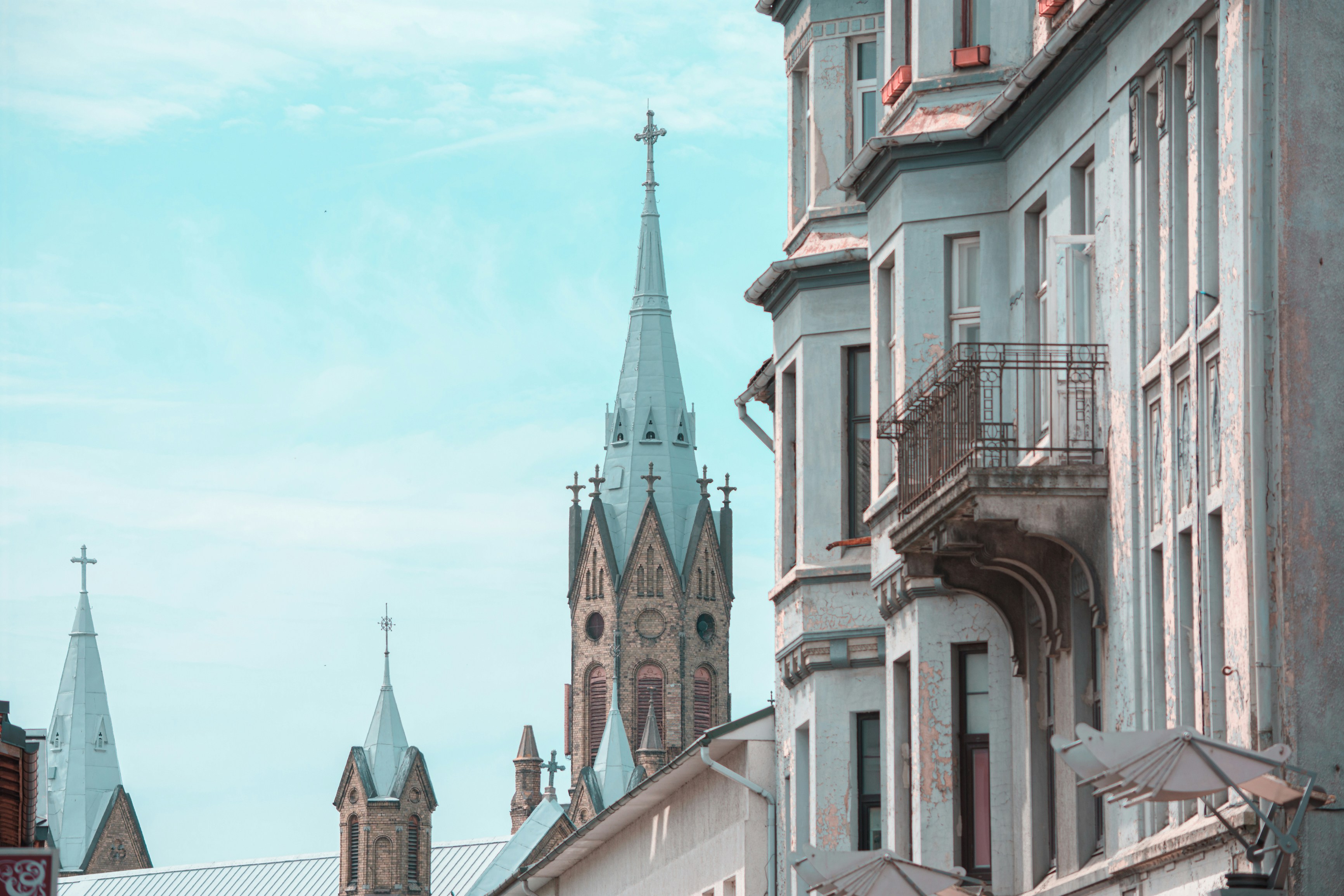 Gothic church spires rise behind ornate urban architecture under a vibrant blue sky.