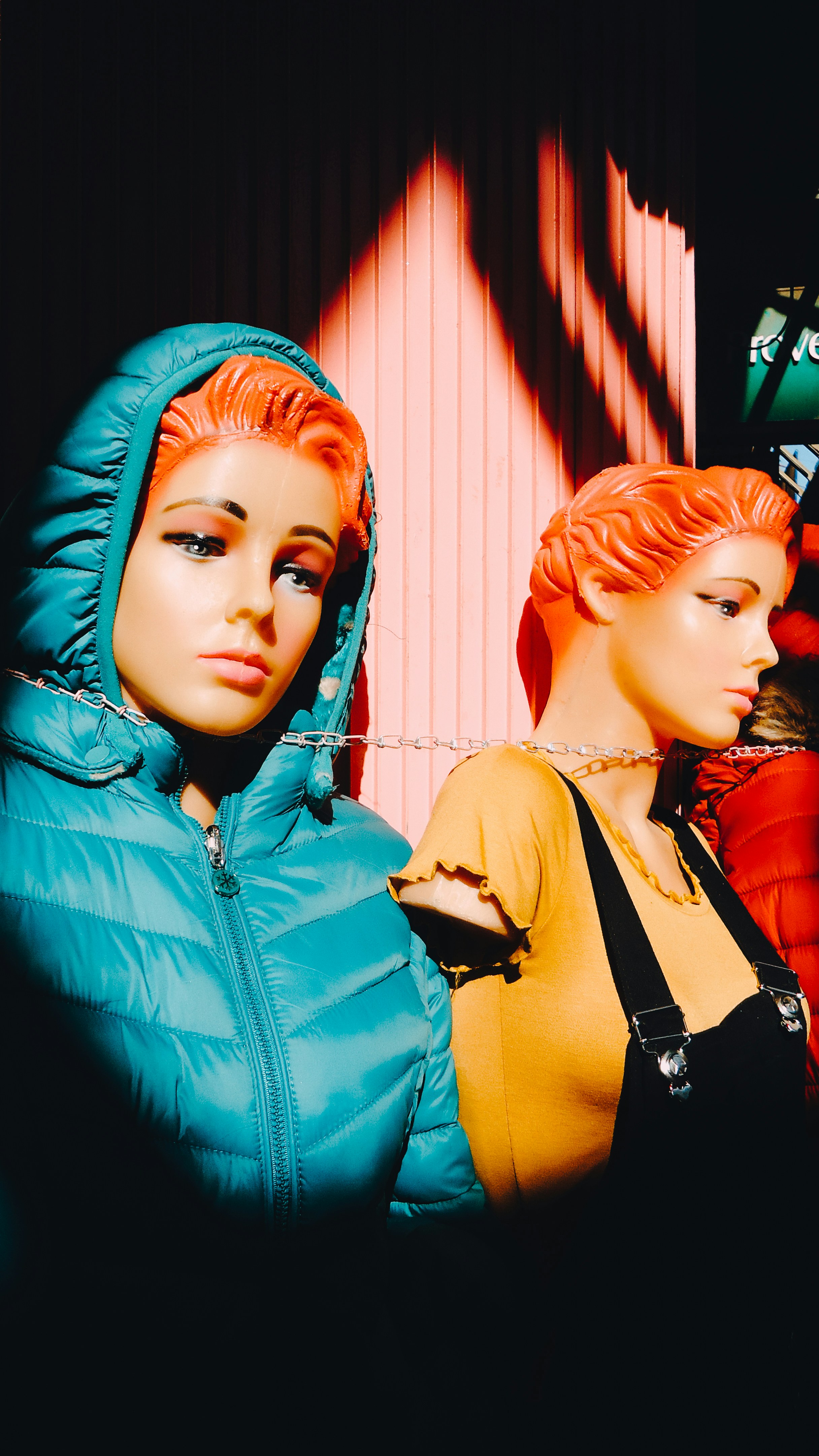 Teal Hoodie, Orange Hair: A Duo of Mannequin Portraits Against Pink Stripes