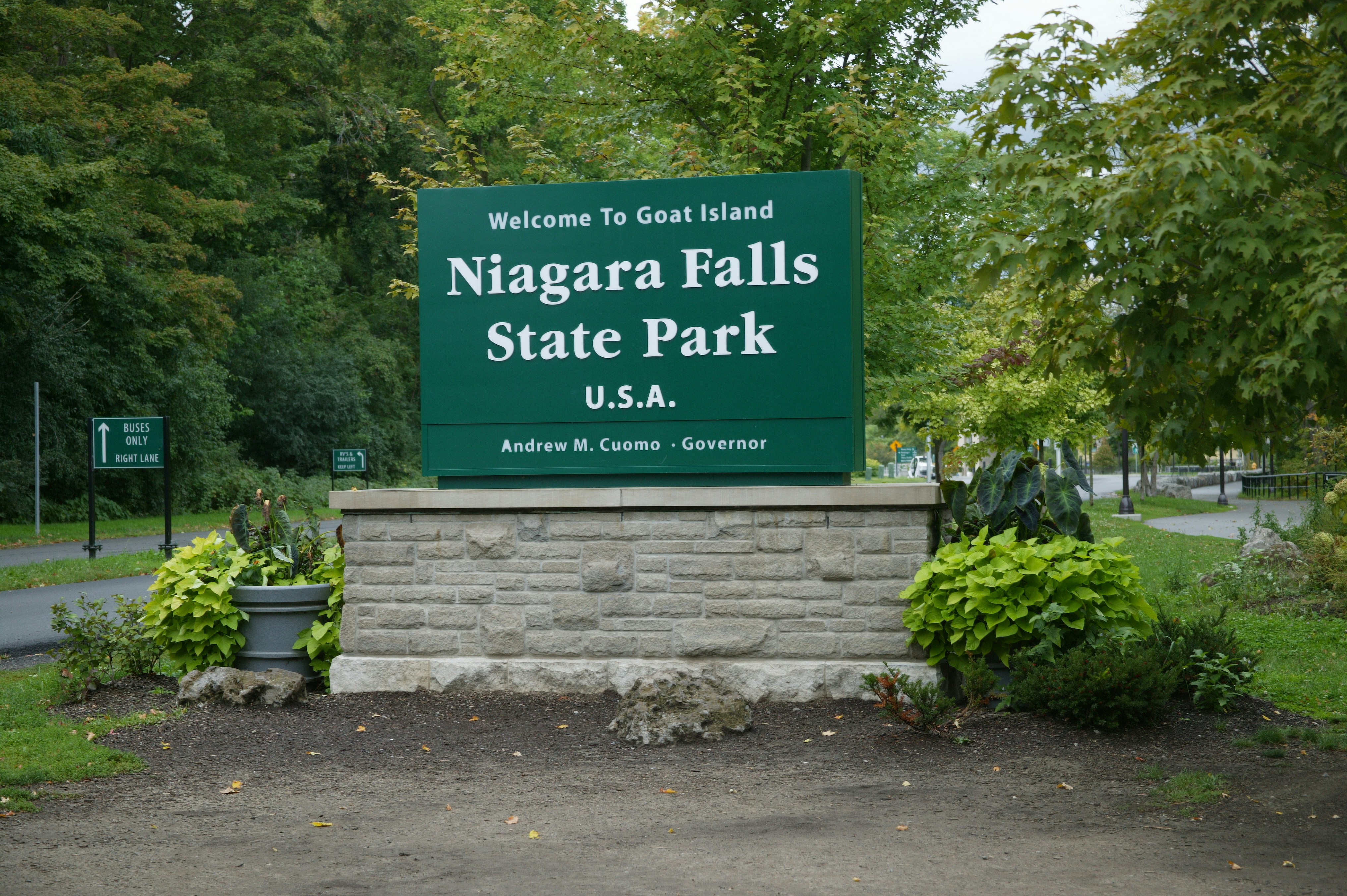 Stone sign welcoming visitors to Niagara Falls State Park surrounded by lush greenery.