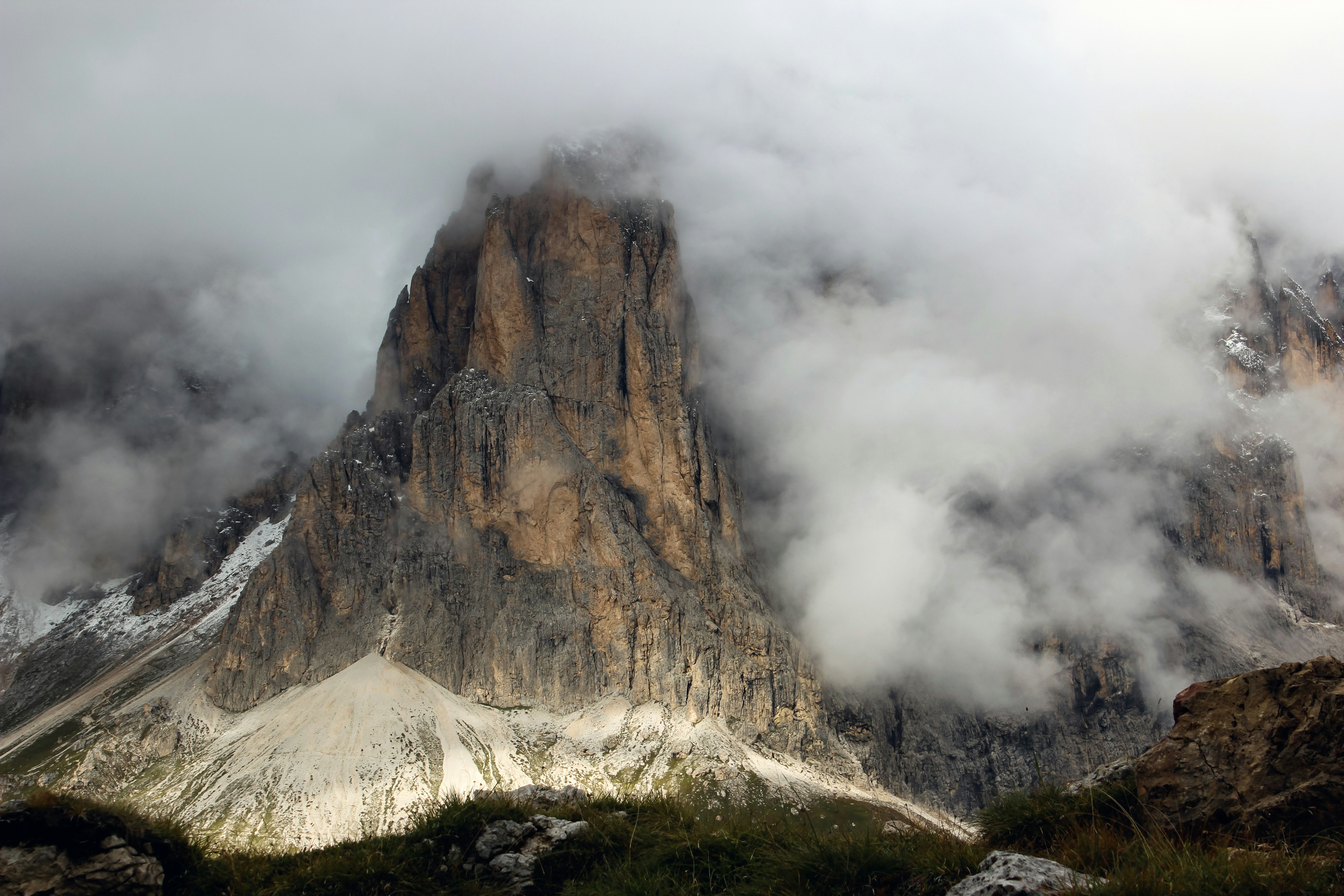 Towering mountain shrouded in mist, revealing rugged cliffs and patches of snow. The ethereal atmosphere enhances the dramatic landscape.