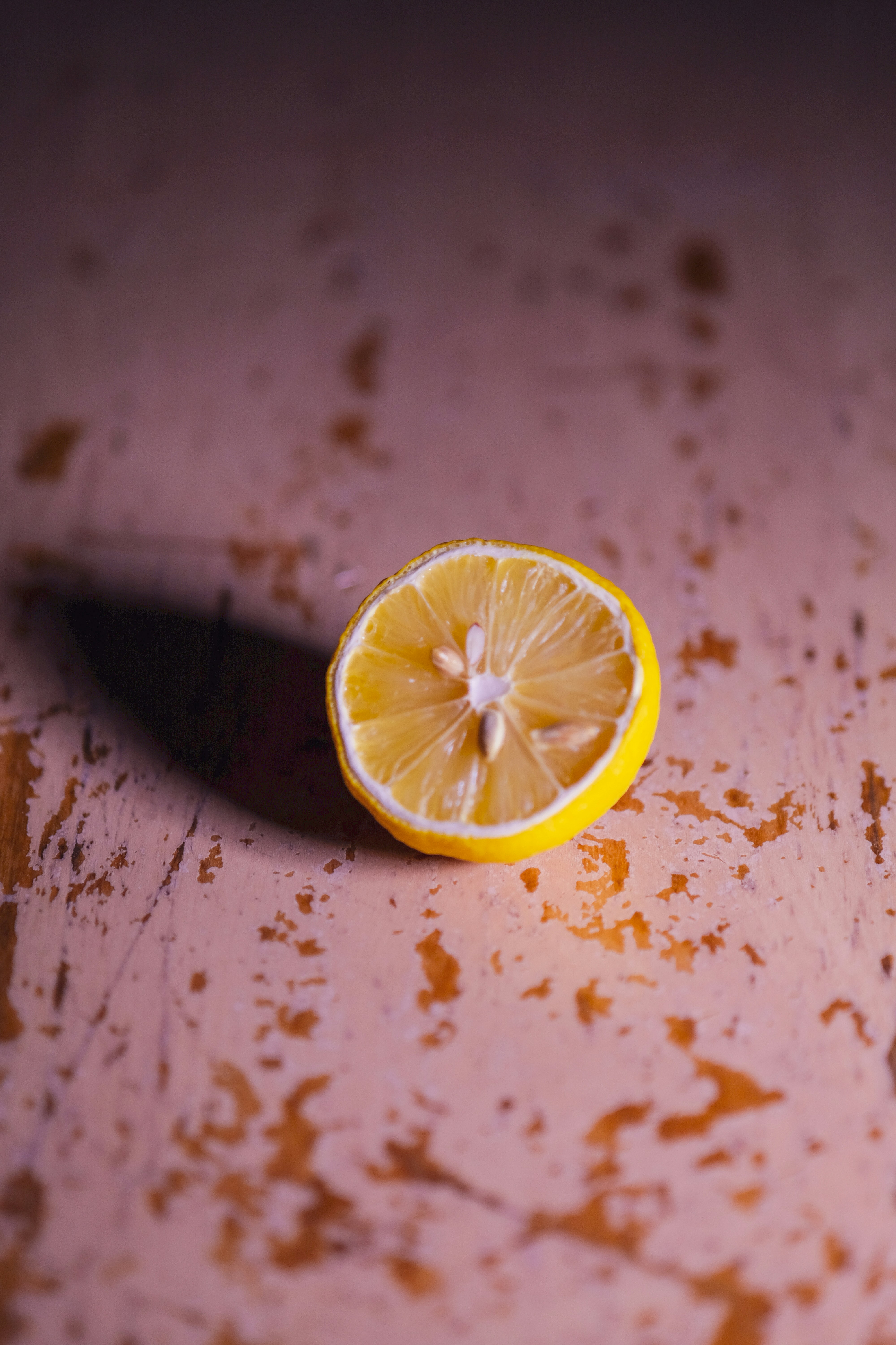 Bright yellow lemon slice resting on a rustic wooden surface, casting a soft shadow.