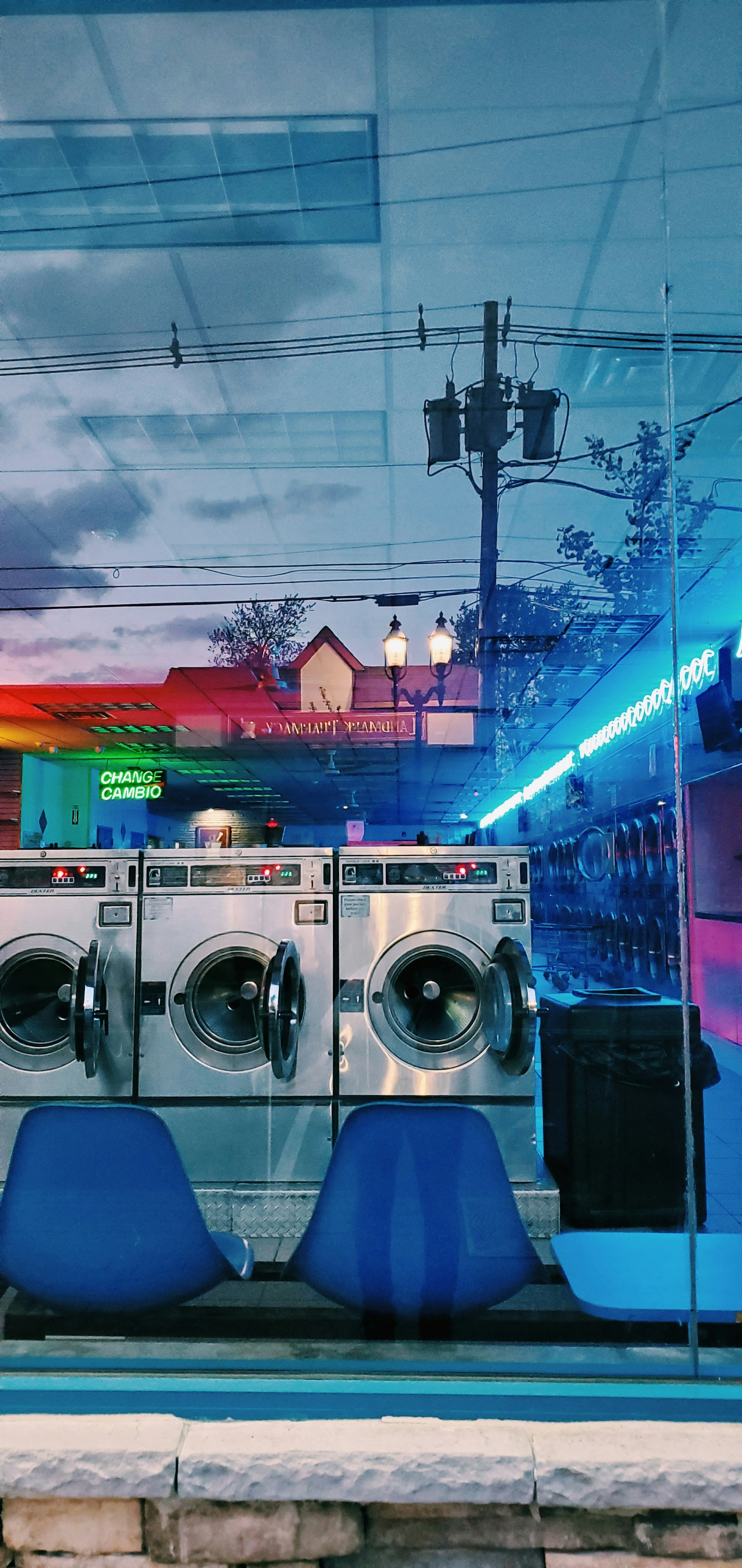 Three Washers Beneath Neon Glass in a Neon-Lit Laundromat
