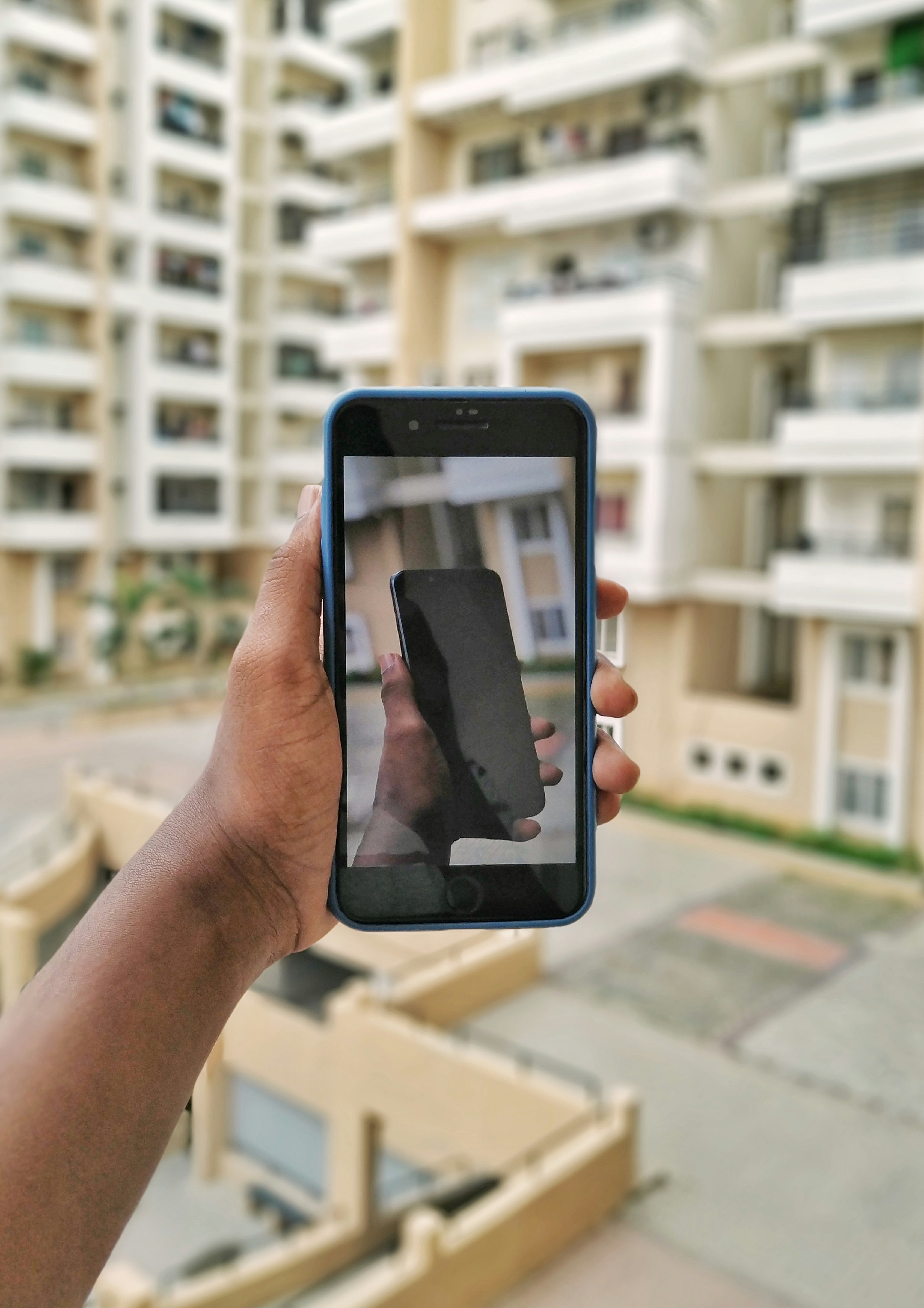 A hand holding a smartphone reflecting a view of an apartment complex, emphasizing the blend of technology and urban living.