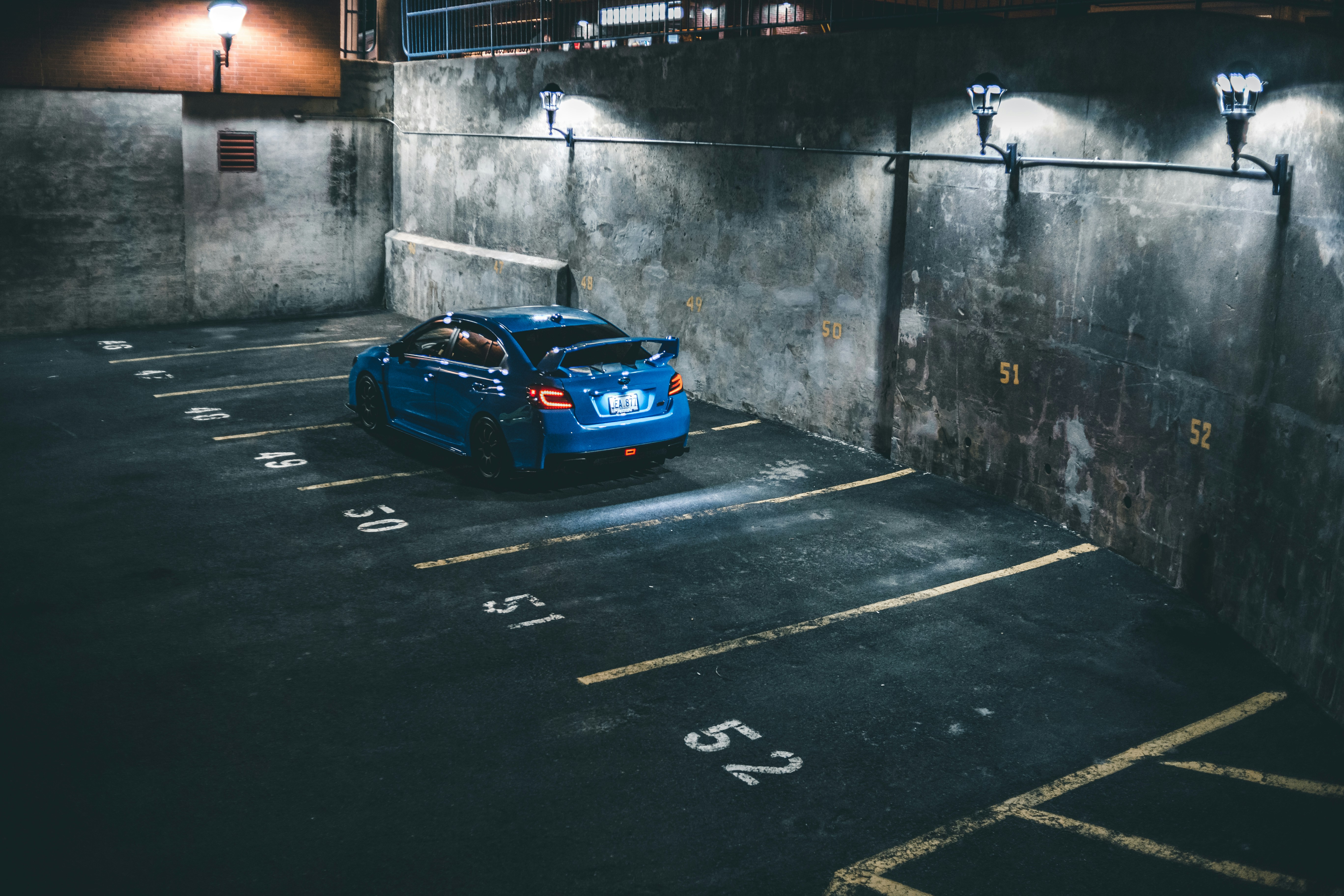 A sleek blue car parked in a dimly lit parking garage, surrounded by empty spaces. The ambiance highlights the contrast between the vehicle and the gritty surroundings.