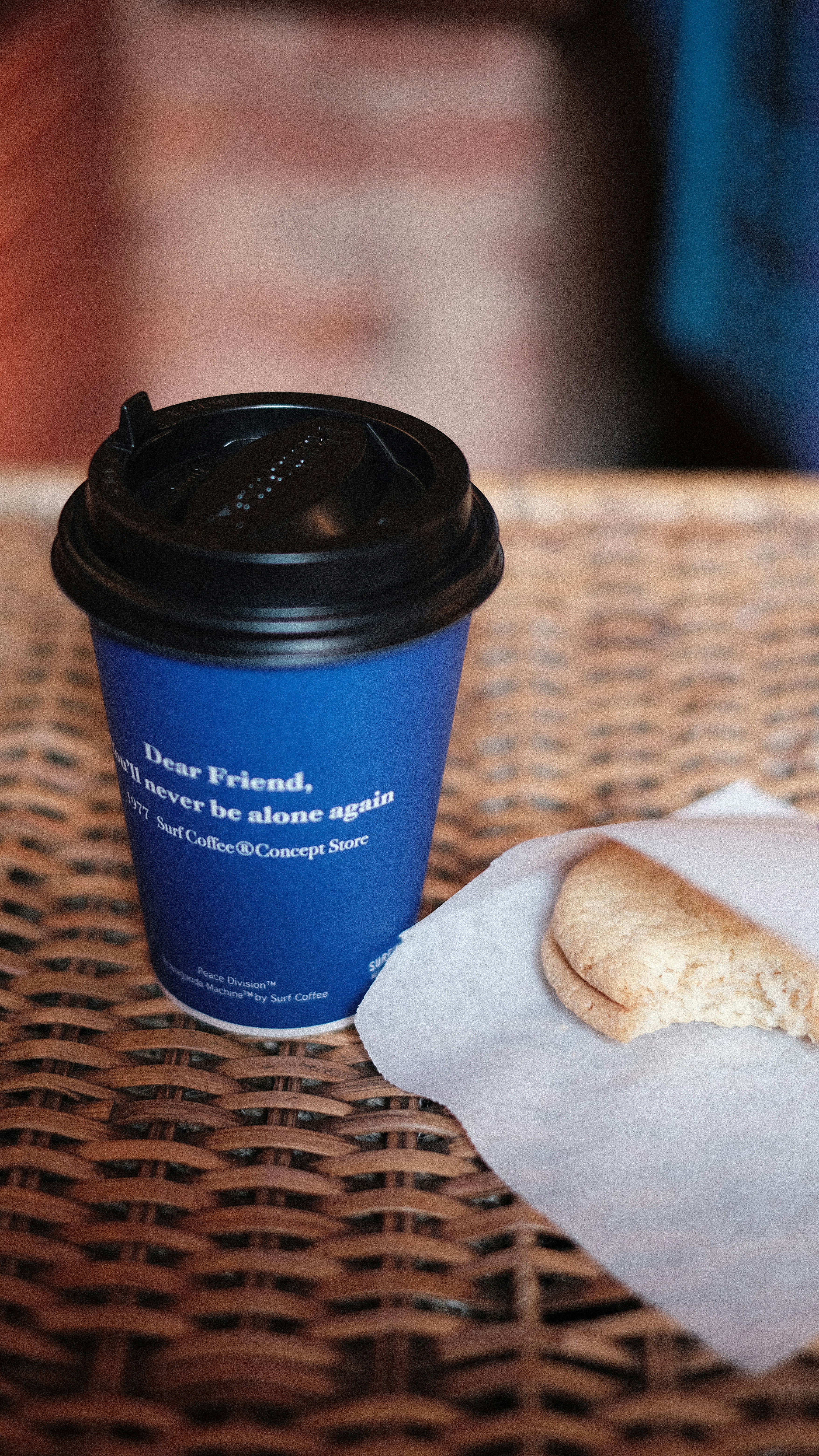 Blue coffee cup with an inspirational message beside a biscuit on a woven table. The warm ambiance invites relaxation.