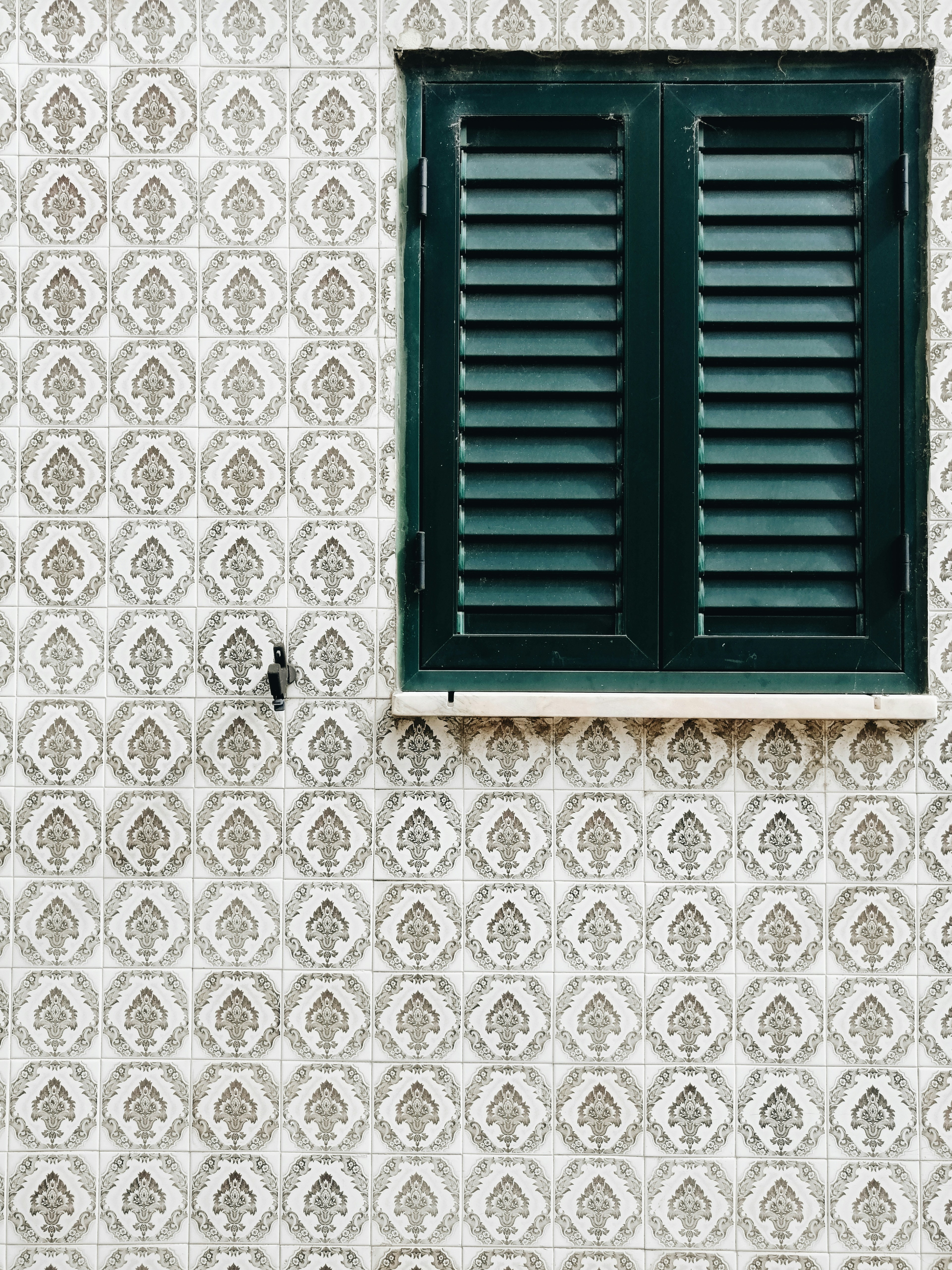 Green shuttered window against a patterned tiled wall, showcasing intricate designs and a hint of history.