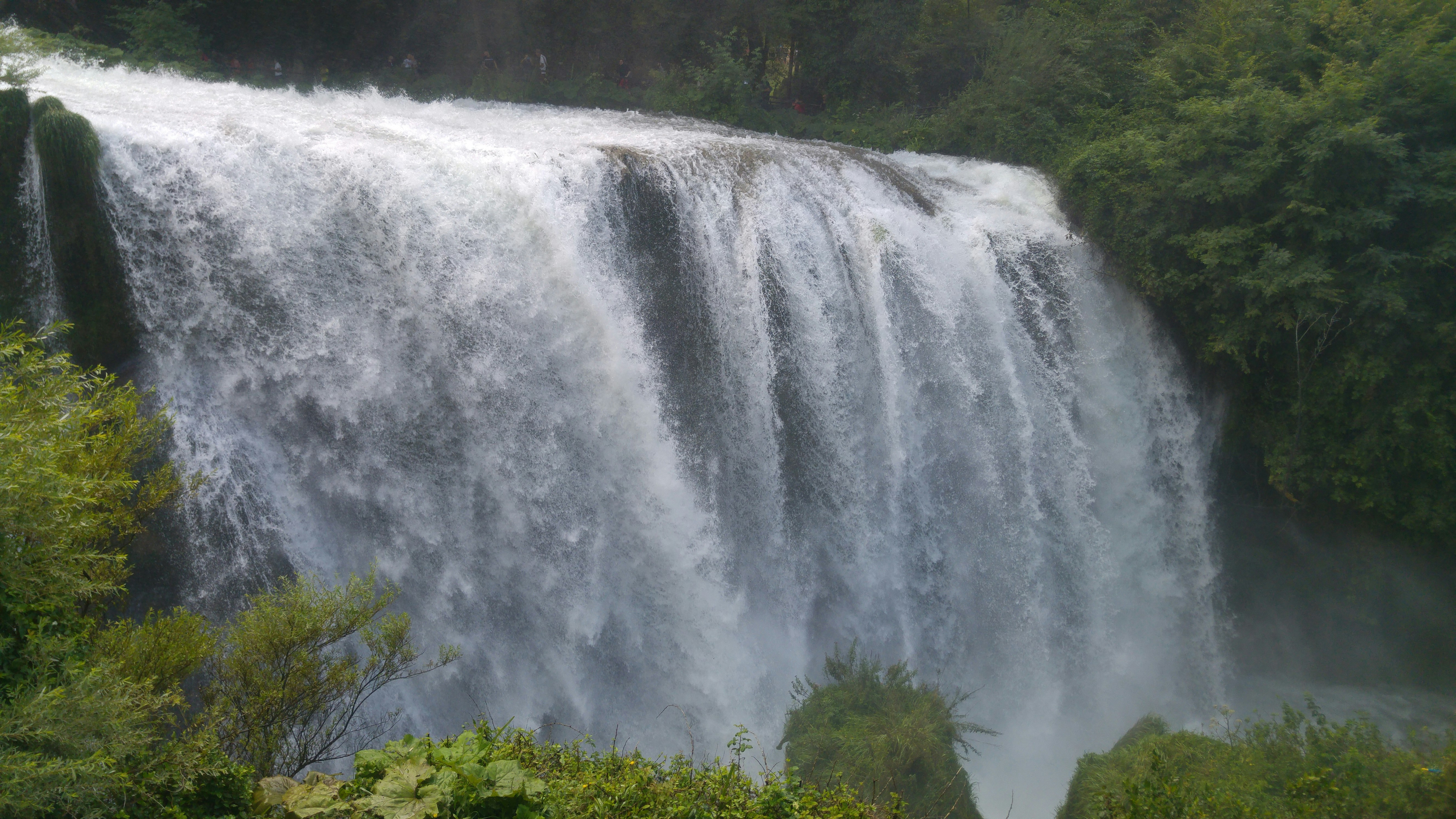Majestic waterfall pouring over rocky ledge, surrounded by lush greenery and mist. A natural spectacle of flowing water.