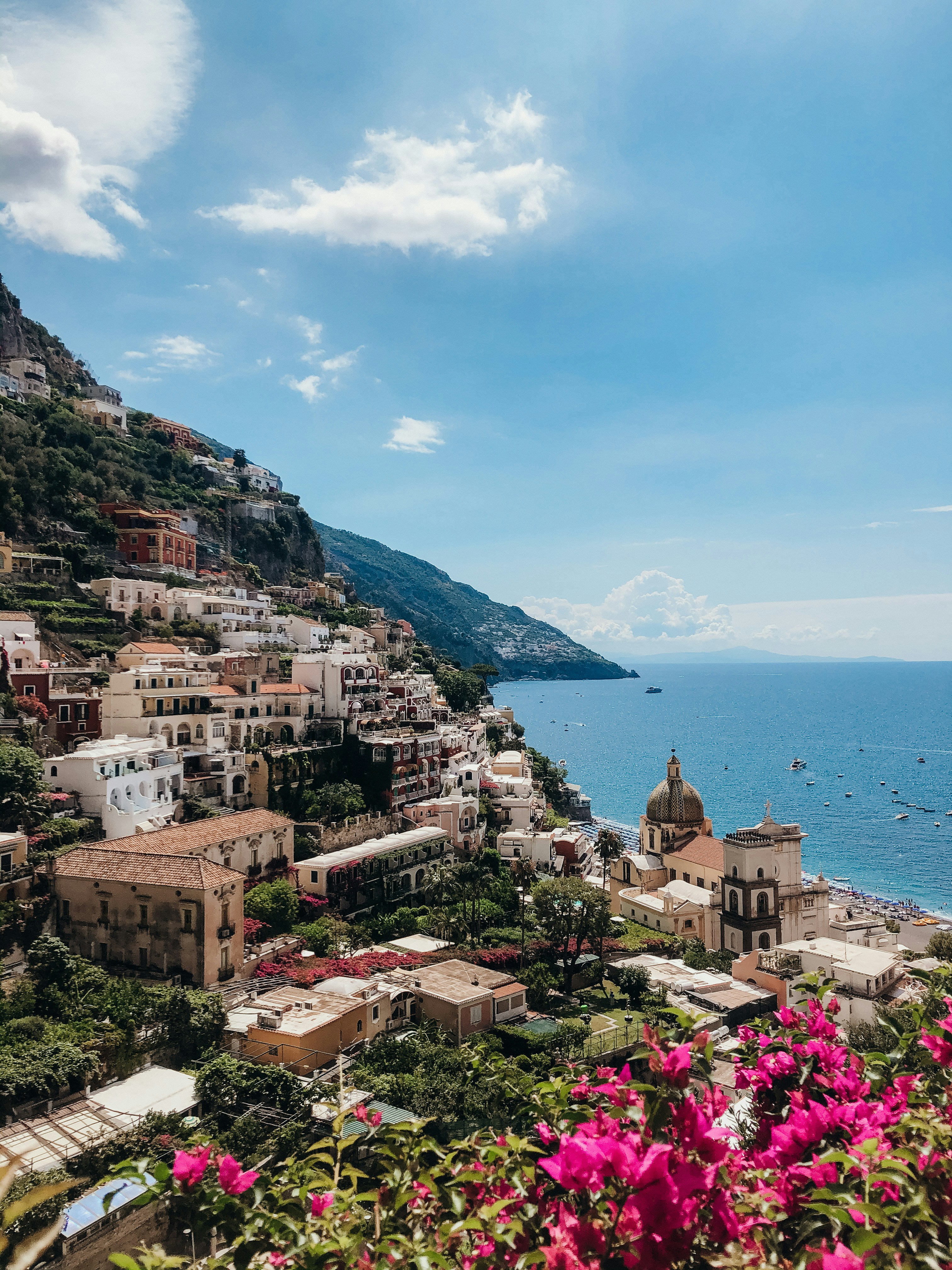 Charming hillside village of Positano, adorned with colorful buildings, lush greenery, and the sparkling Mediterranean Sea in the background.