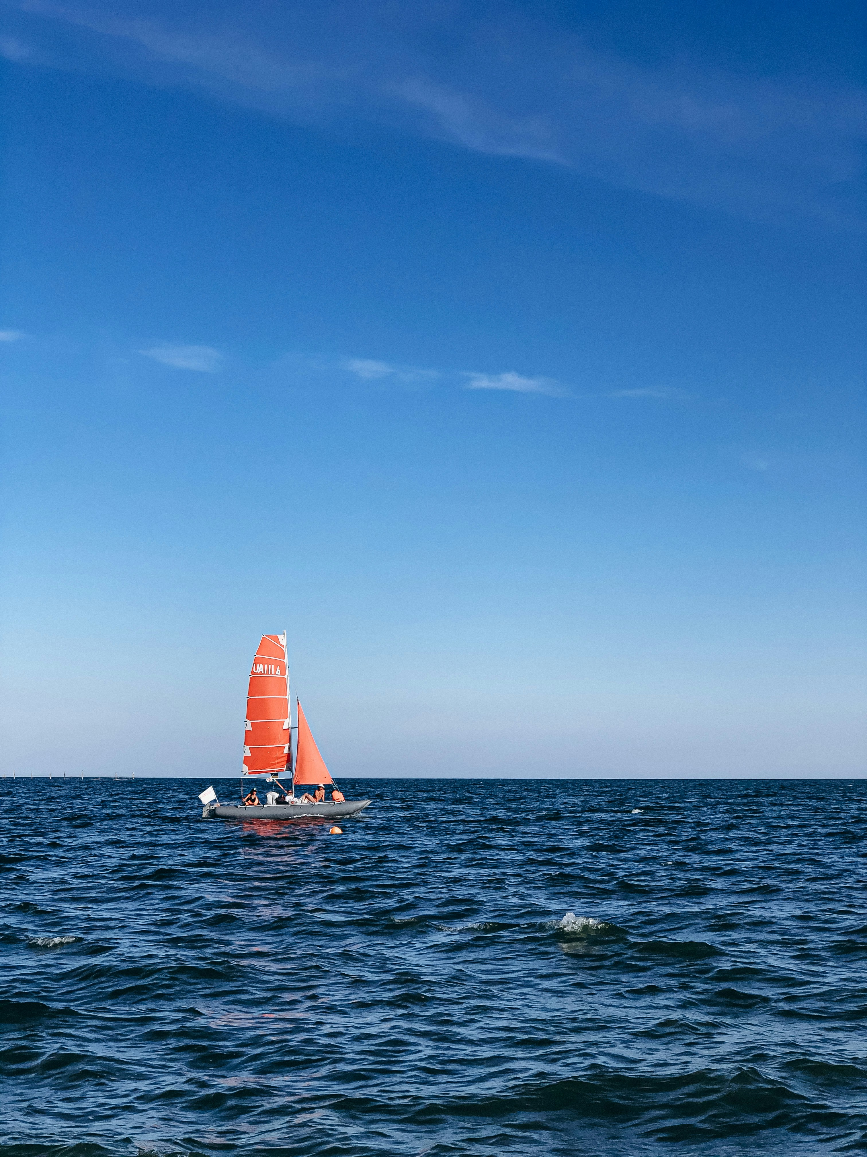 Crimson Sails on a Wide Blue Expanse: A Small Vessel in Quiet Ocean Light