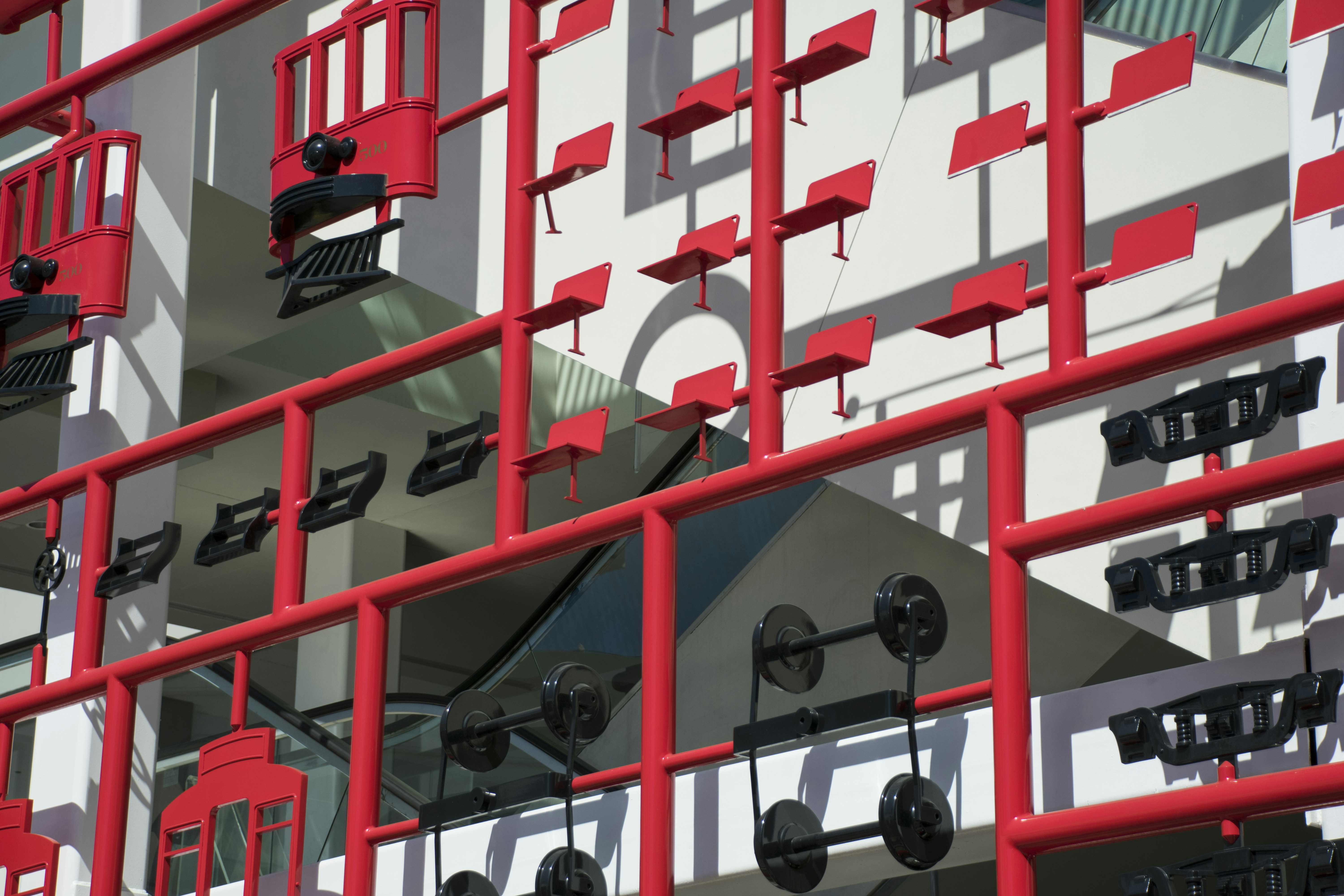 Crimson Lattice Framing a Glass Facade: A Lone Figure Amid Geometric Reflections