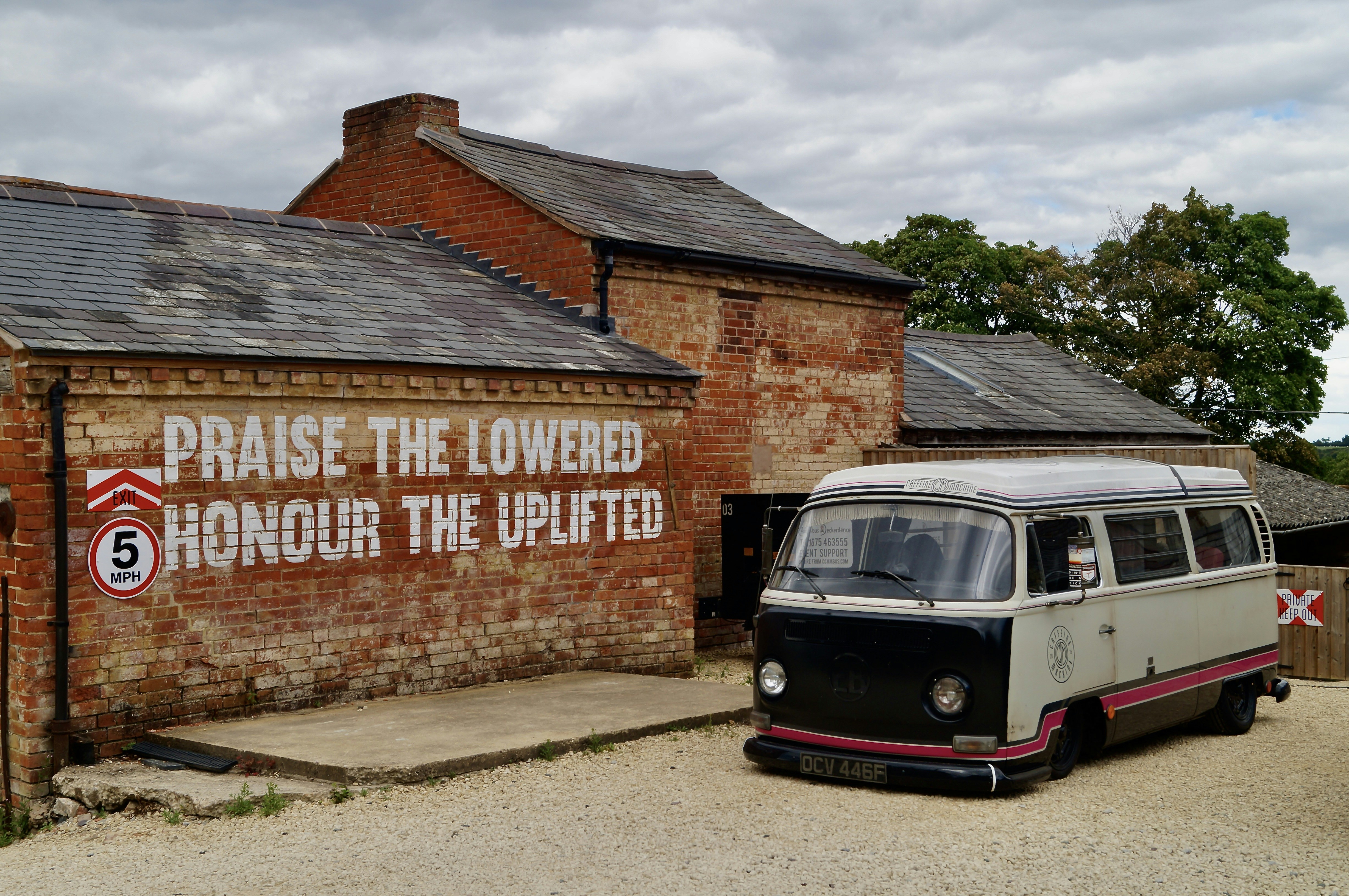 Retro van parked beside an old brick building with philosophical graffiti under a cloudy sky.