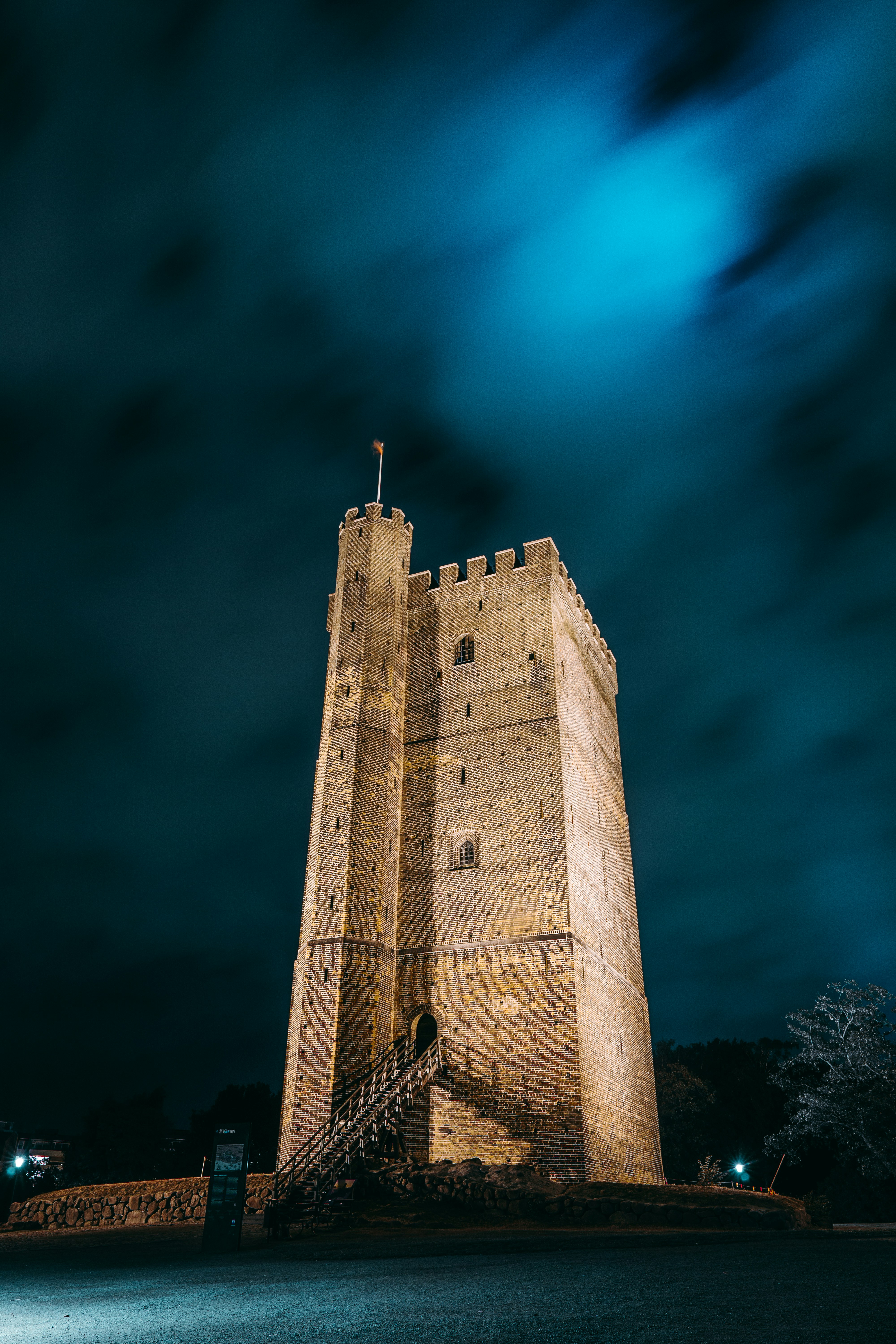 Illuminated medieval tower against a dramatic night sky with swirling clouds.