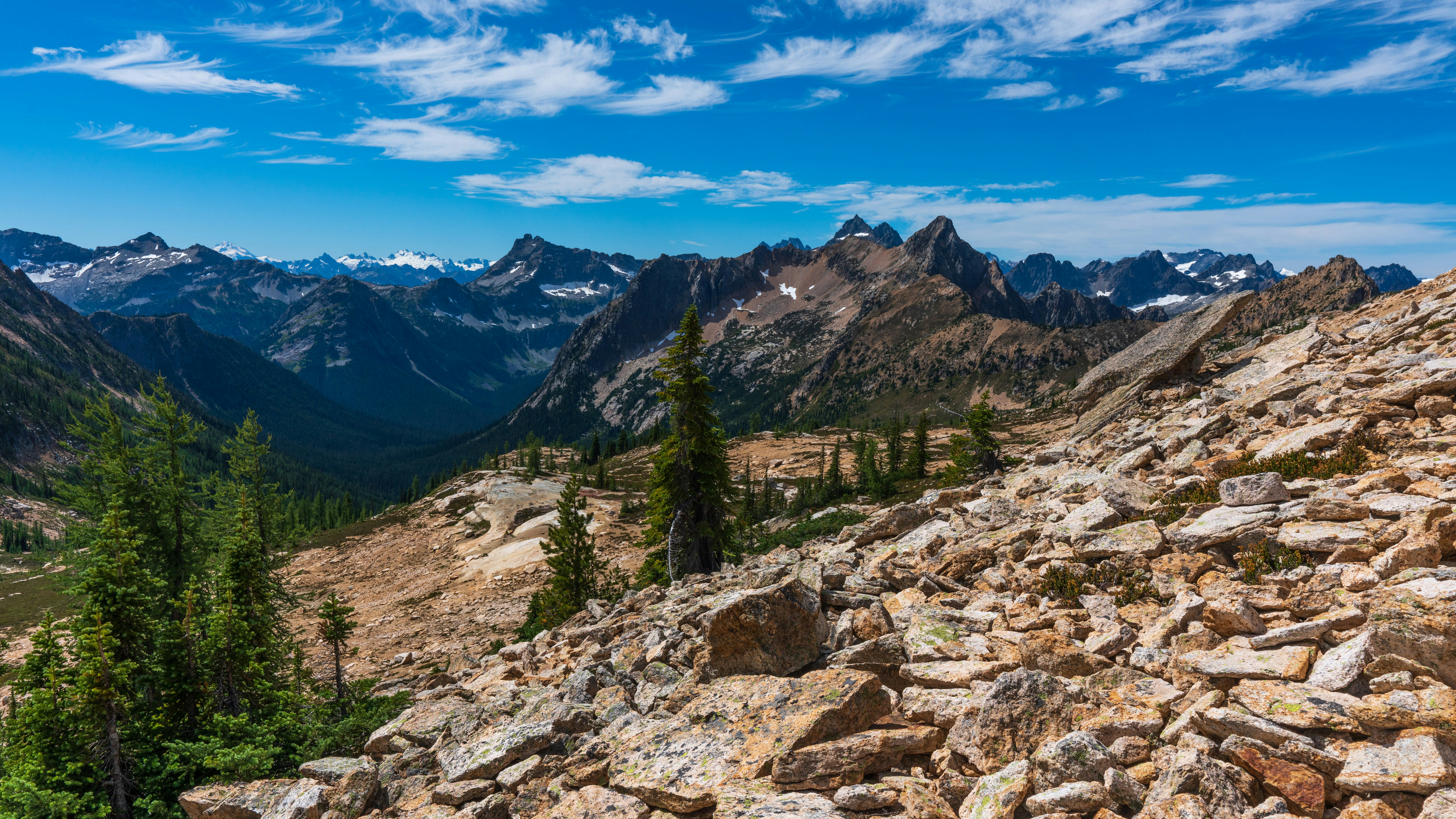 Rocky mountain terrain with sparse green trees under a bright blue sky.