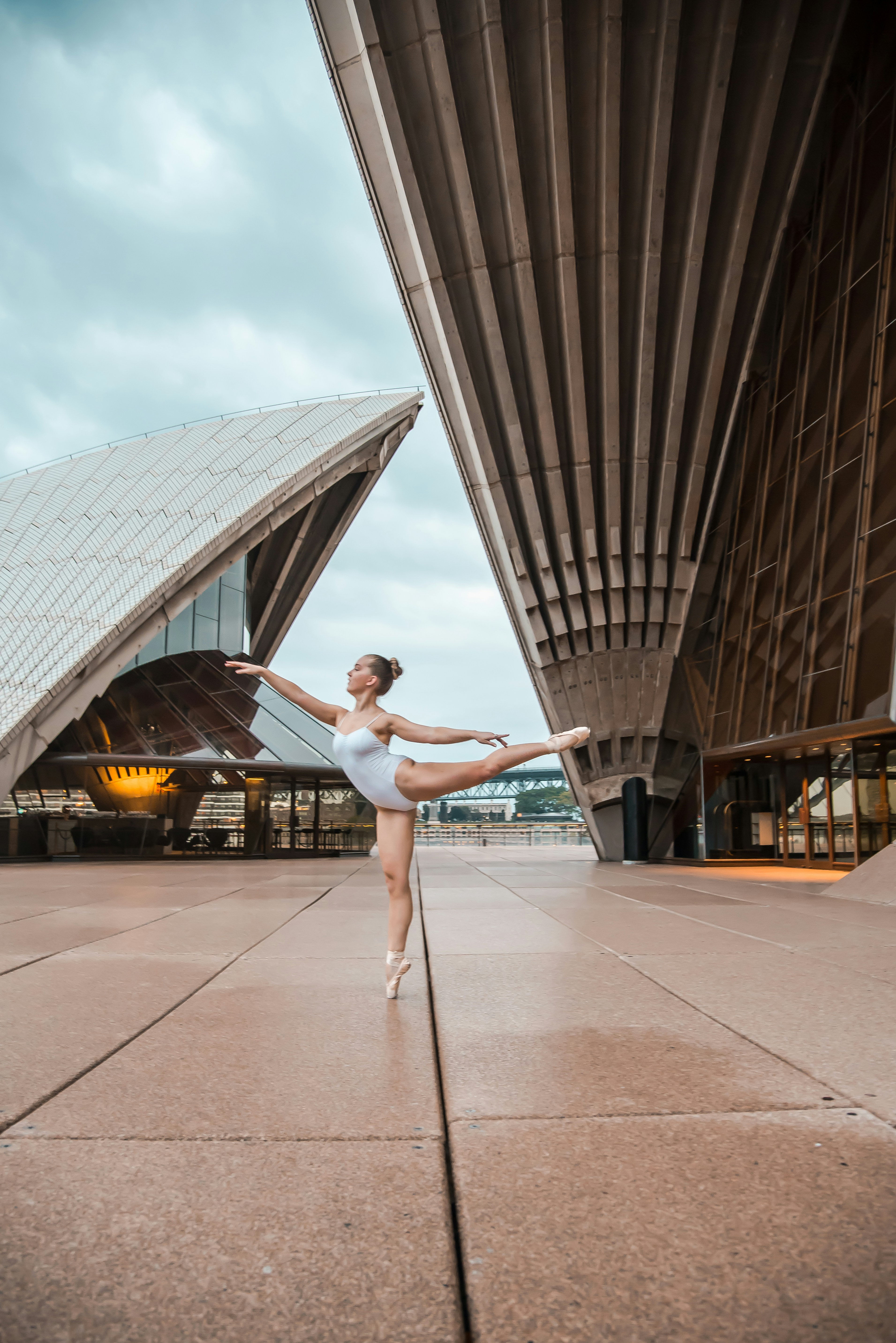 Ballet dancer executing an elegant pose against the backdrop of modern architectural structures. The scene captures the fusion of art and design.