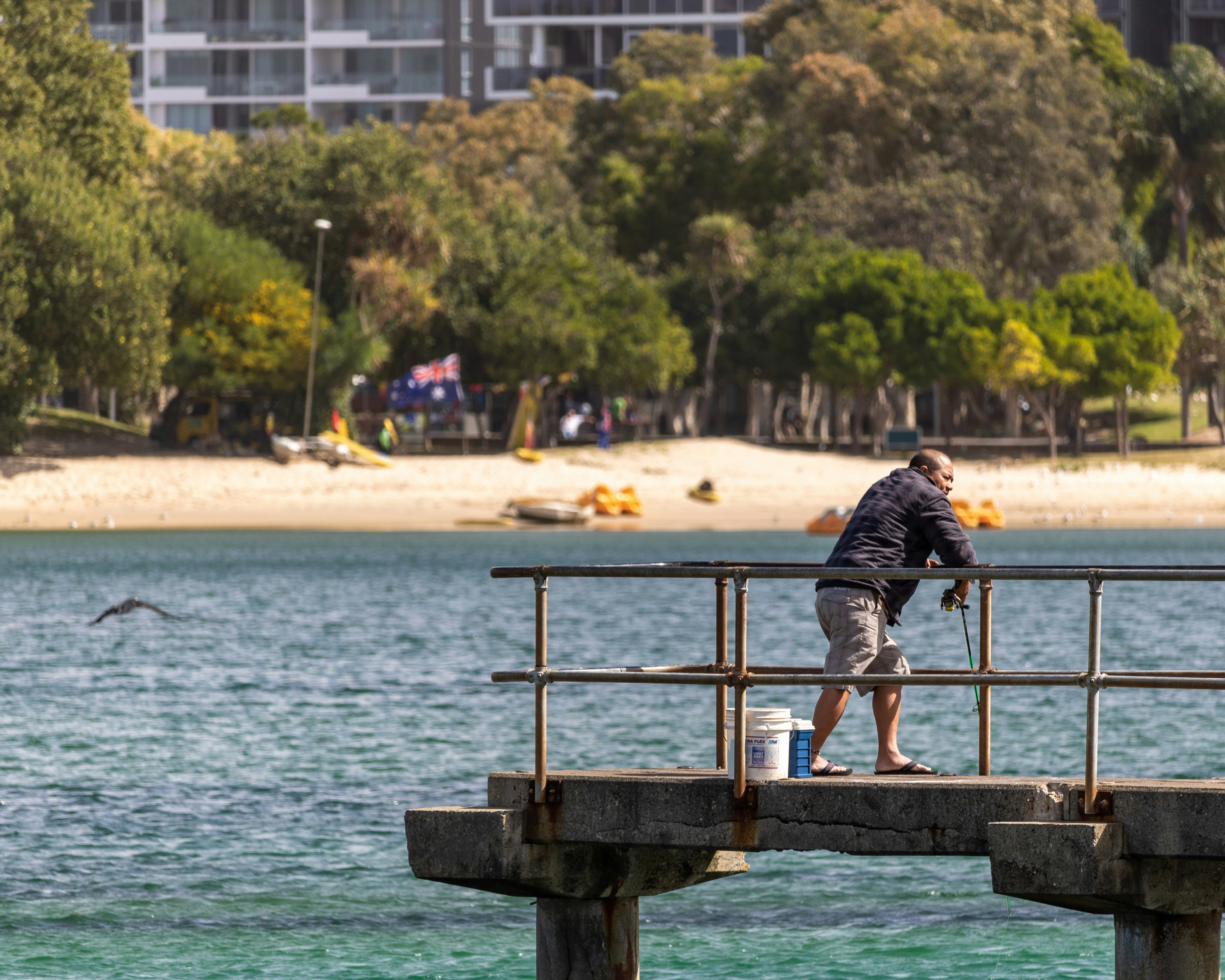 Distant shoreline, close-up on a lone fisherman at the pier