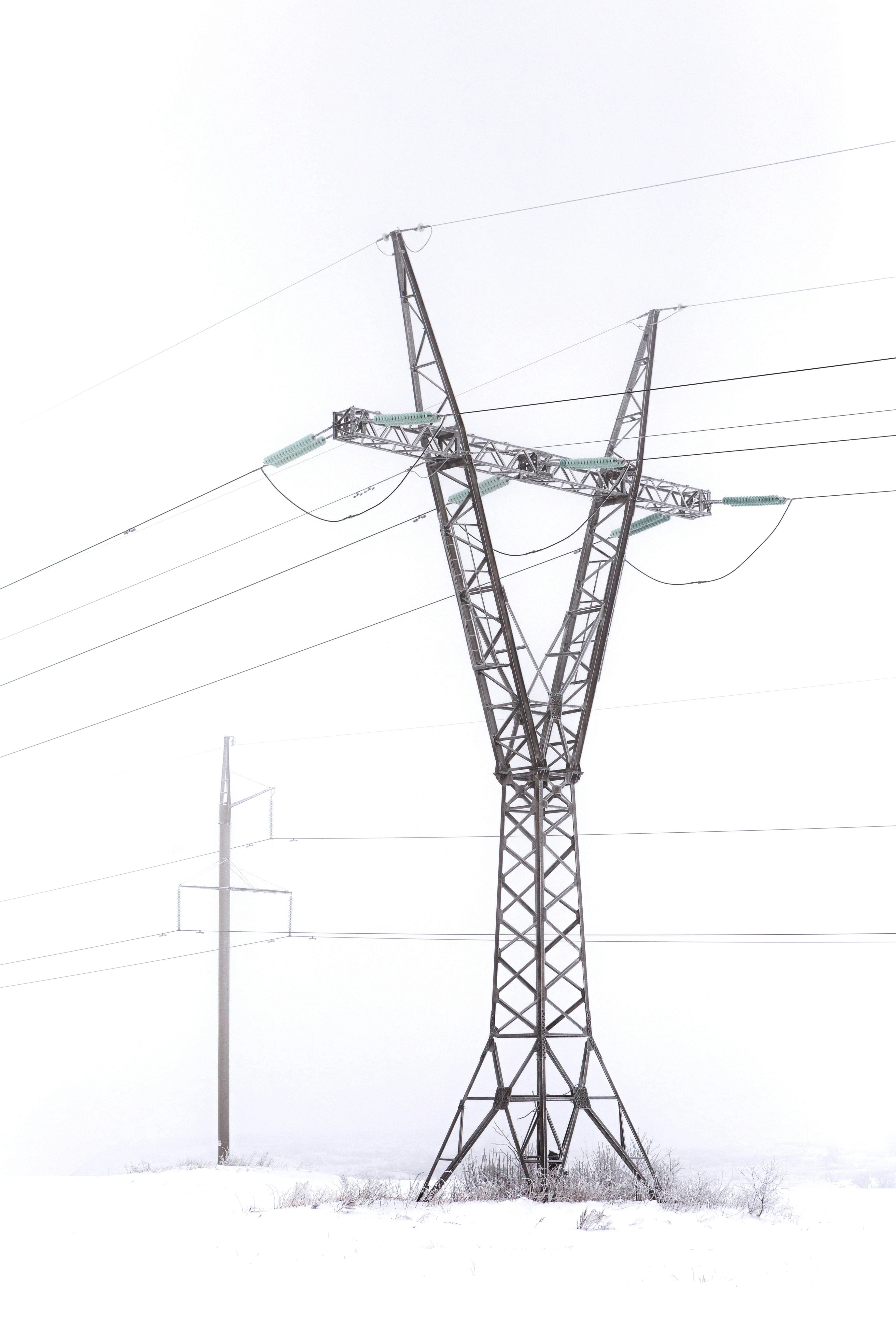 A towering power line structure rises against a stark, foggy backdrop, emphasizing the contrast between industrial design and natural elements.