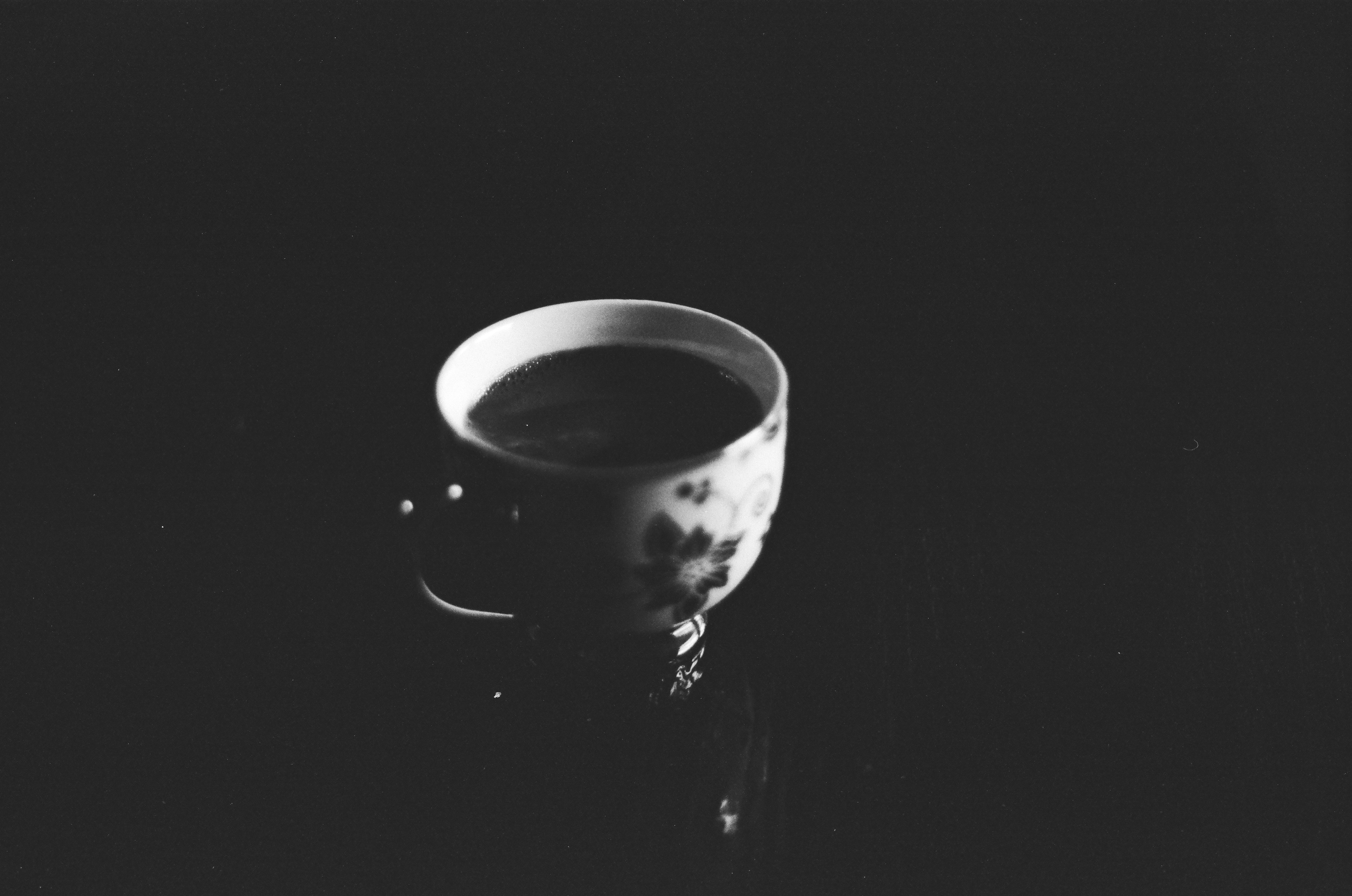 A delicate porcelain cup filled with dark liquid, set against a stark black background, emphasizing its form and texture.