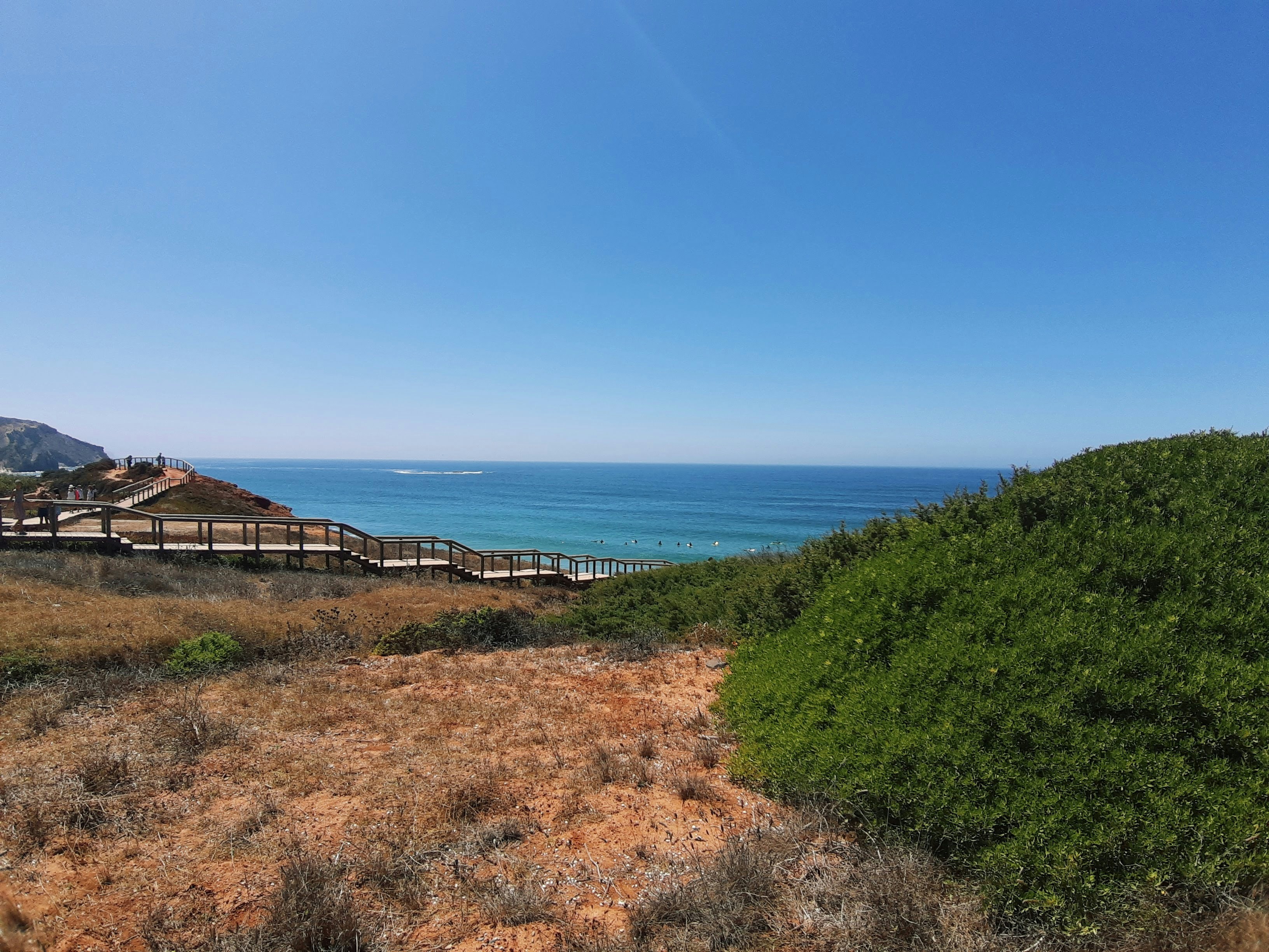Vibrant ocean view framed by rugged cliffs and lush greenery under a clear blue sky.