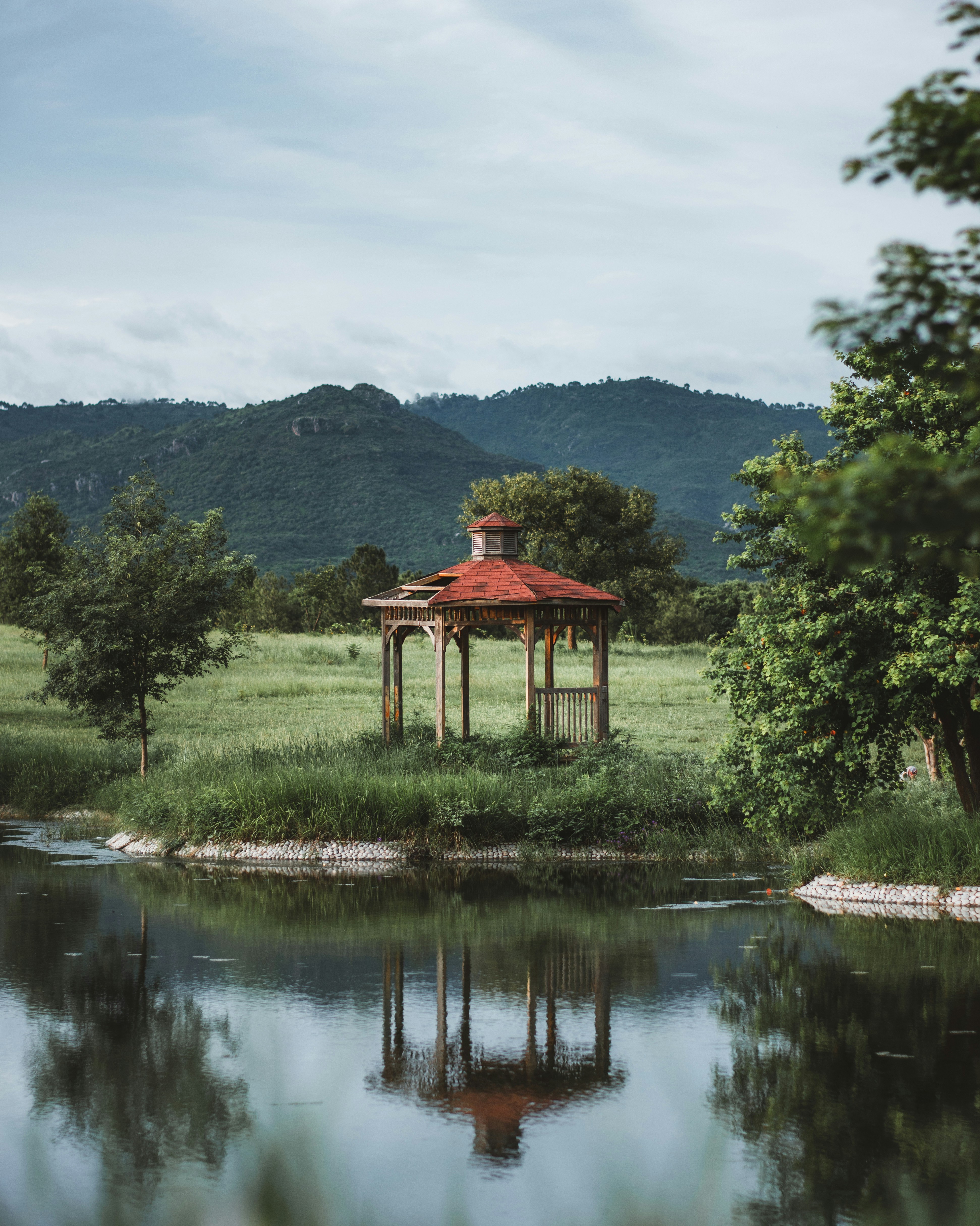 Red-roofed Gazebo Framed by Lake and Hills