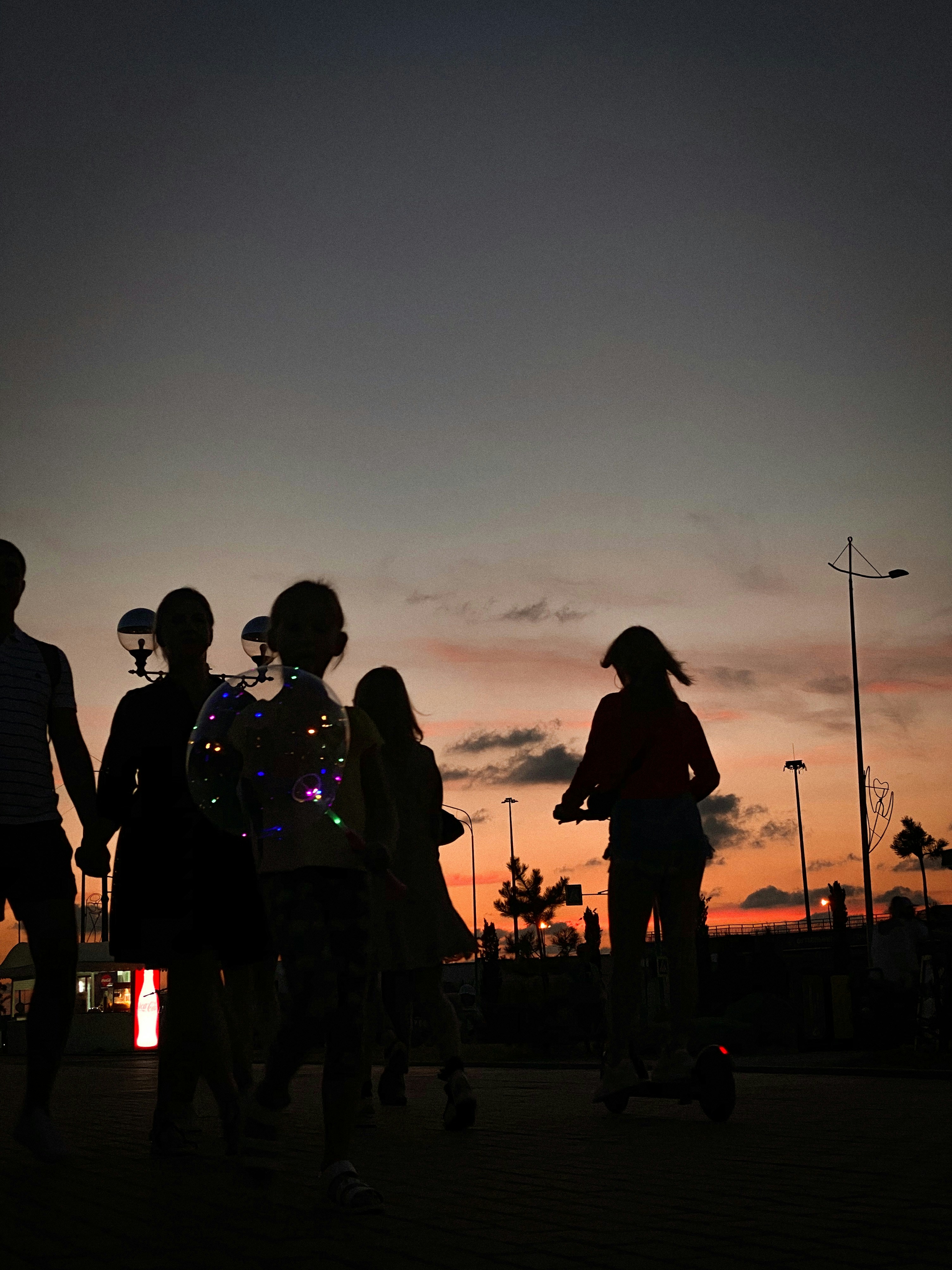 Kids in silhouette chase the last light of a sunset at the waterfront