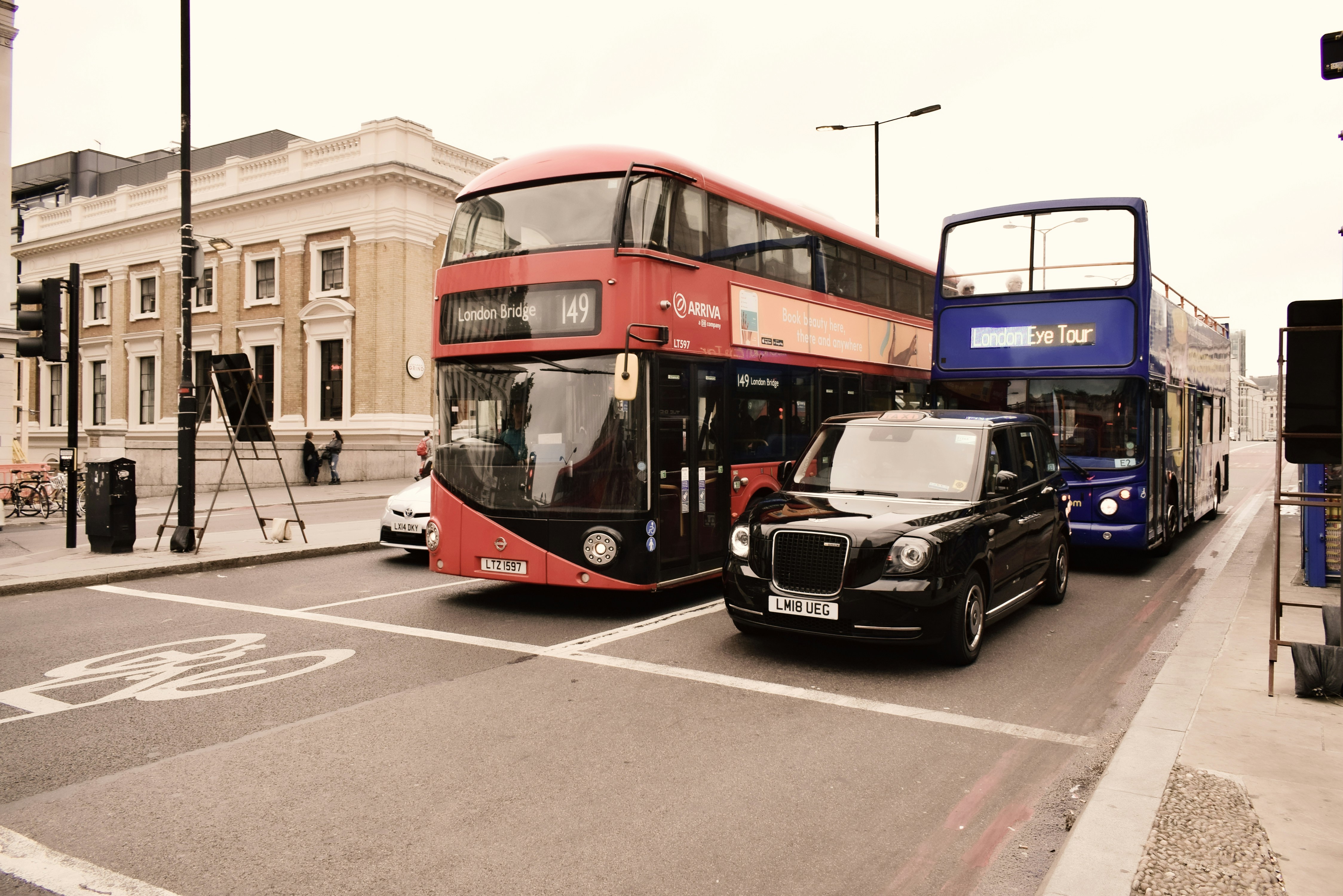 Red and blue double-decker buses alongside a black cab on a city street.