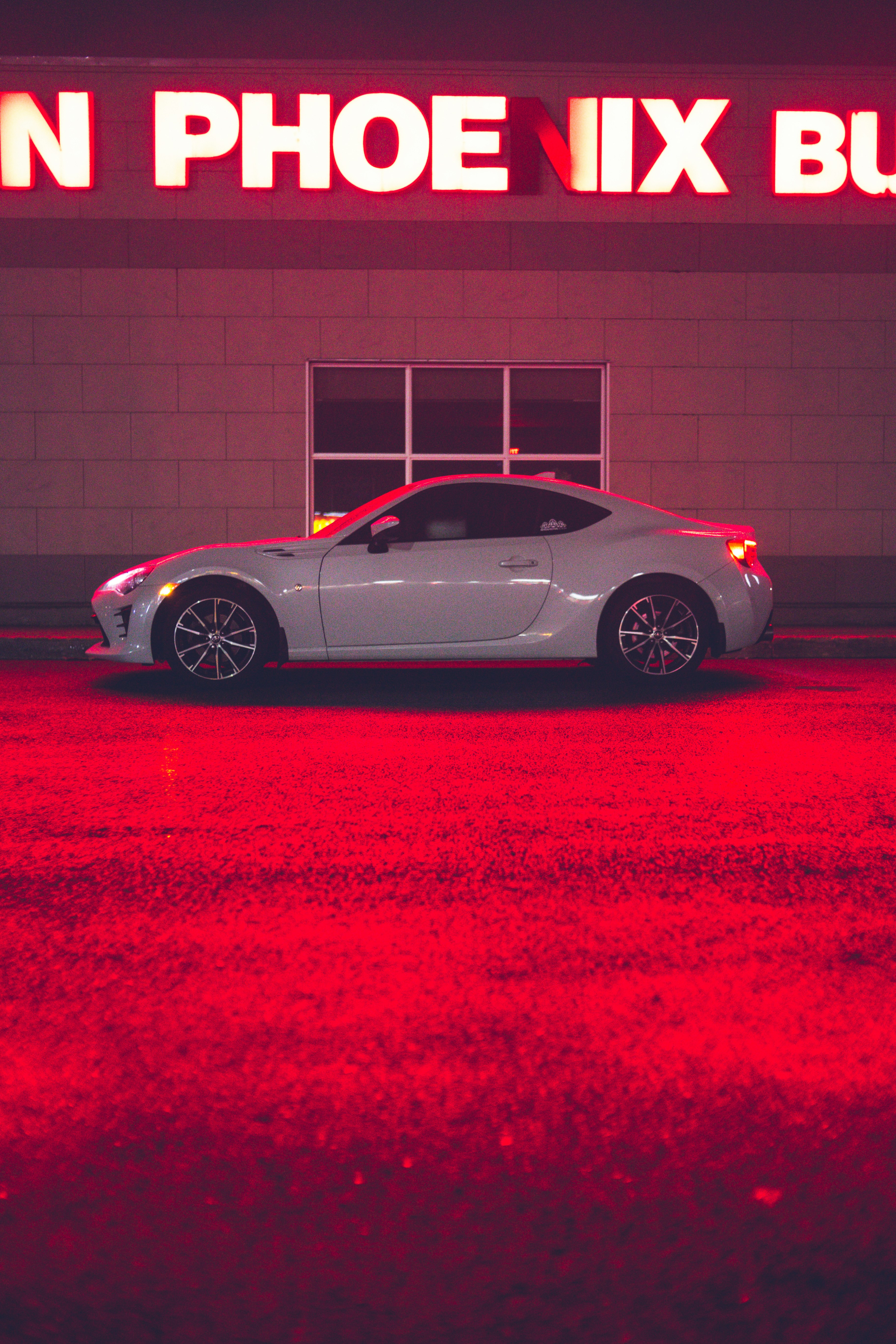 Crimson Neon Reflections: A Silver Sports Car Under Night Lights