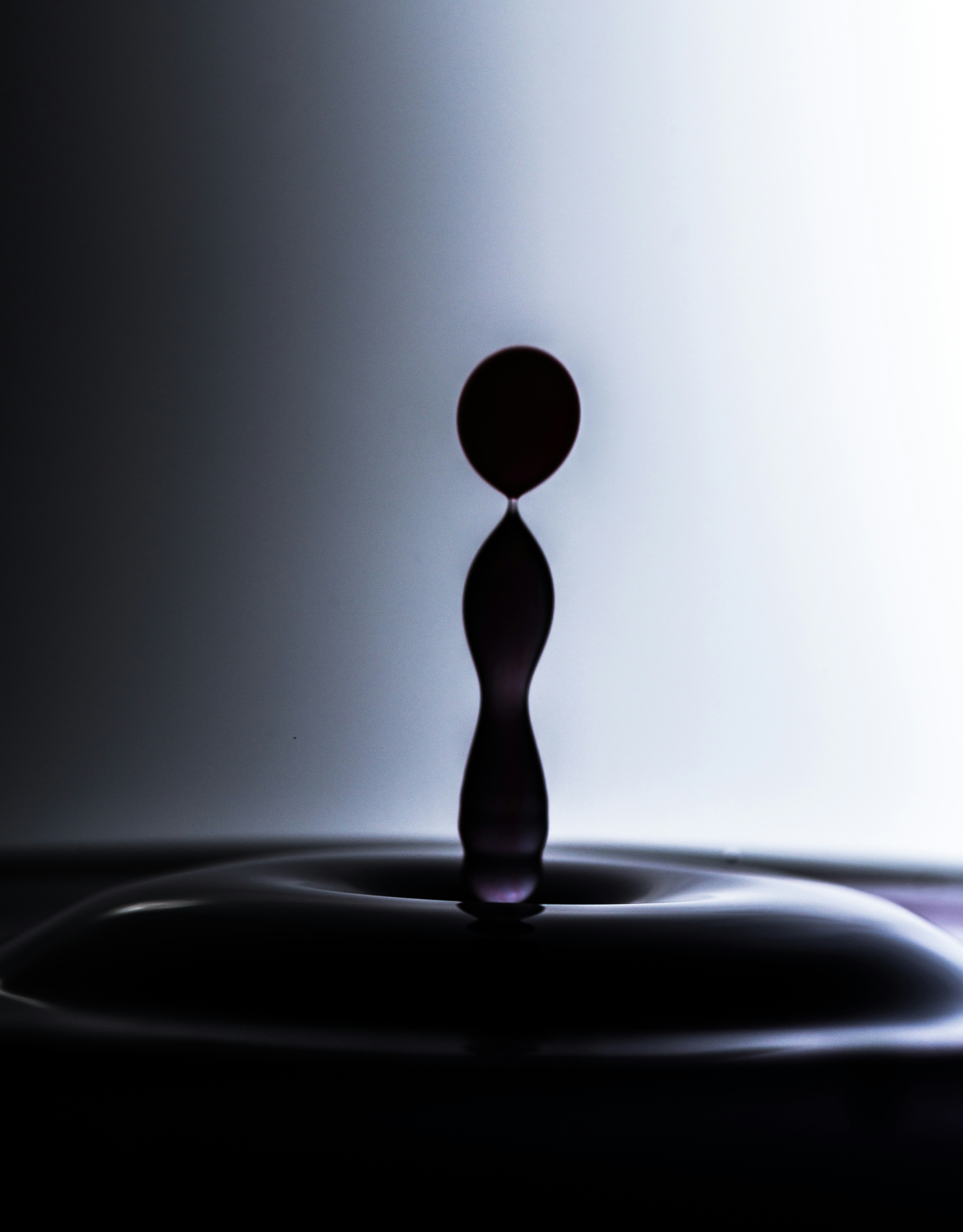 A droplet poised in mid-air above a rippling surface, showcasing the elegance of fluid dynamics. The high-contrast backdrop emphasizes the delicate structure of the droplet.