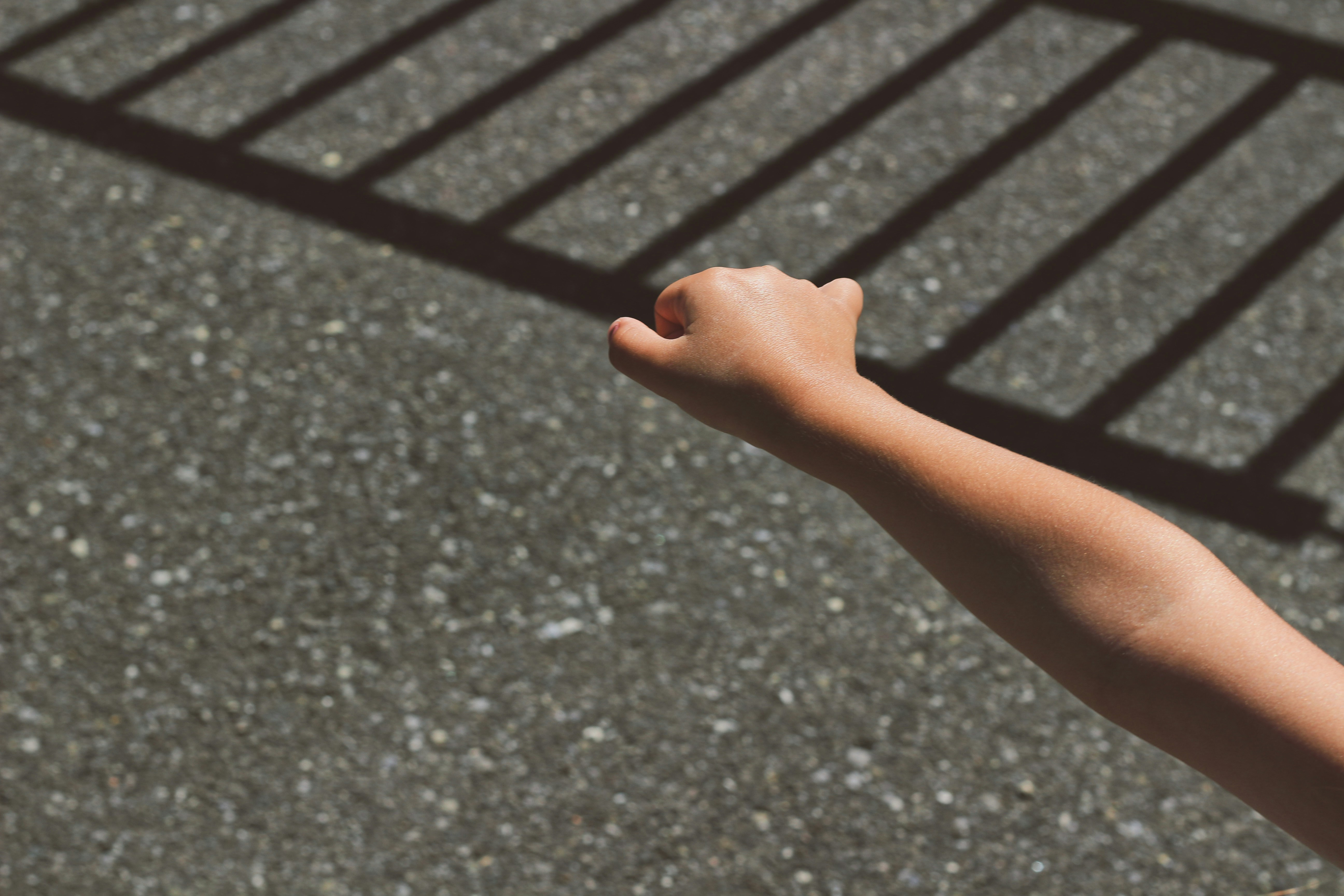 Arm Across a Gravel Canvas: Sunlit Skin Meets Diagonal Rail Shadows