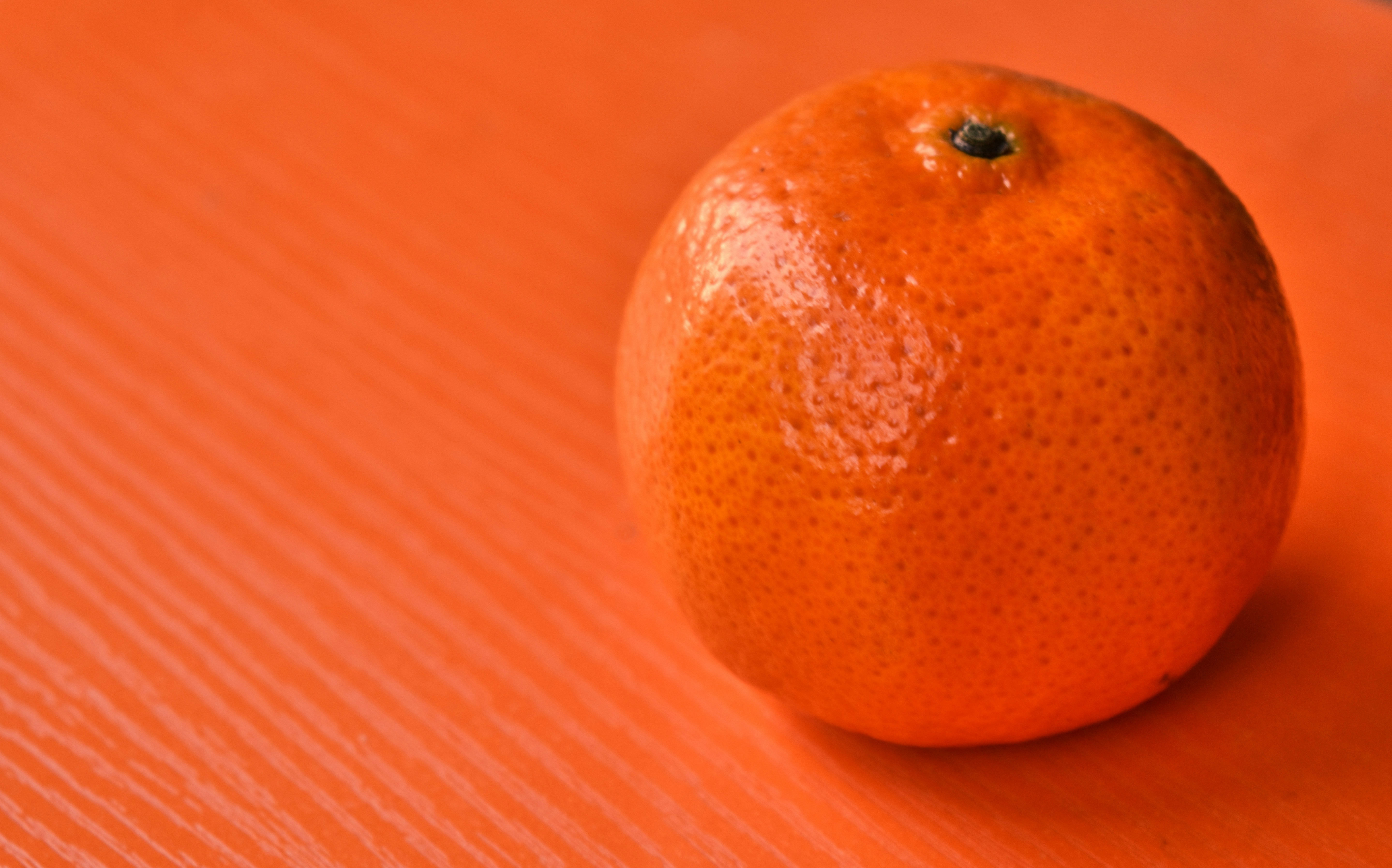 A single orange resting on a textured orange surface, highlighting the fruit's natural sheen and dimples.
