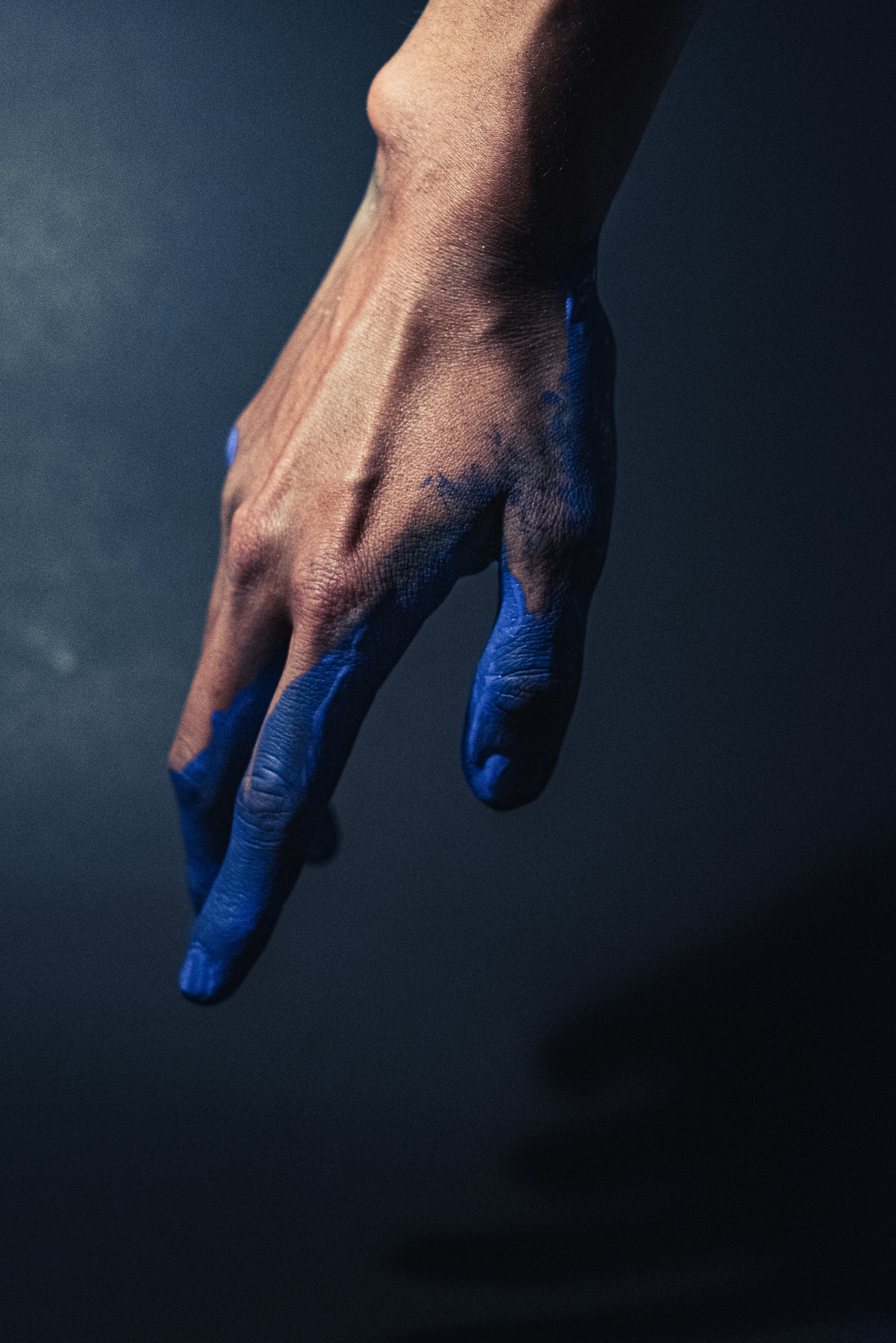A hand with blue paint reaching out against a dark background, capturing a moment of artistic expression.