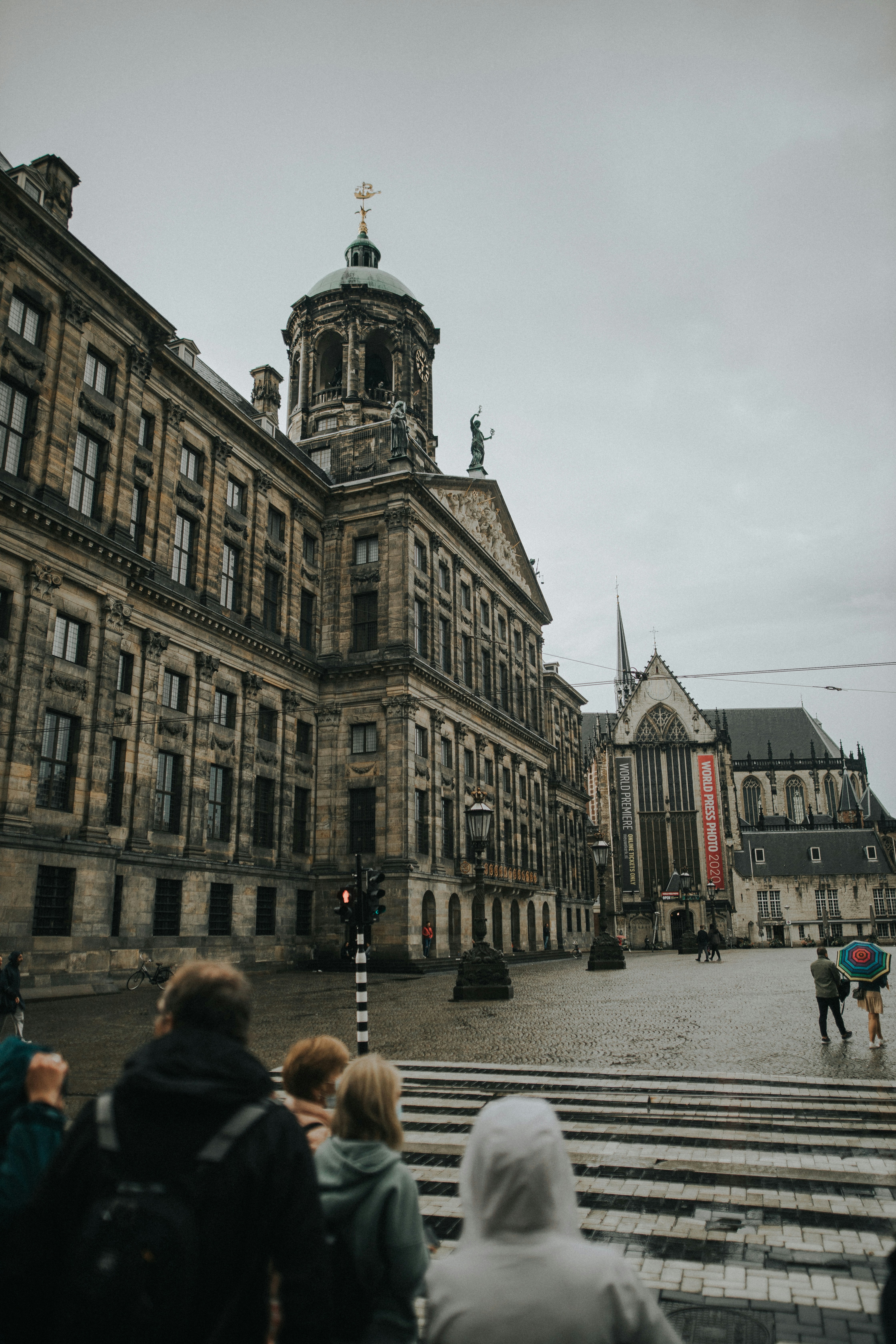 Historic architecture framed against a cloudy sky, with pedestrians crossing a cobblestone street in the foreground.
