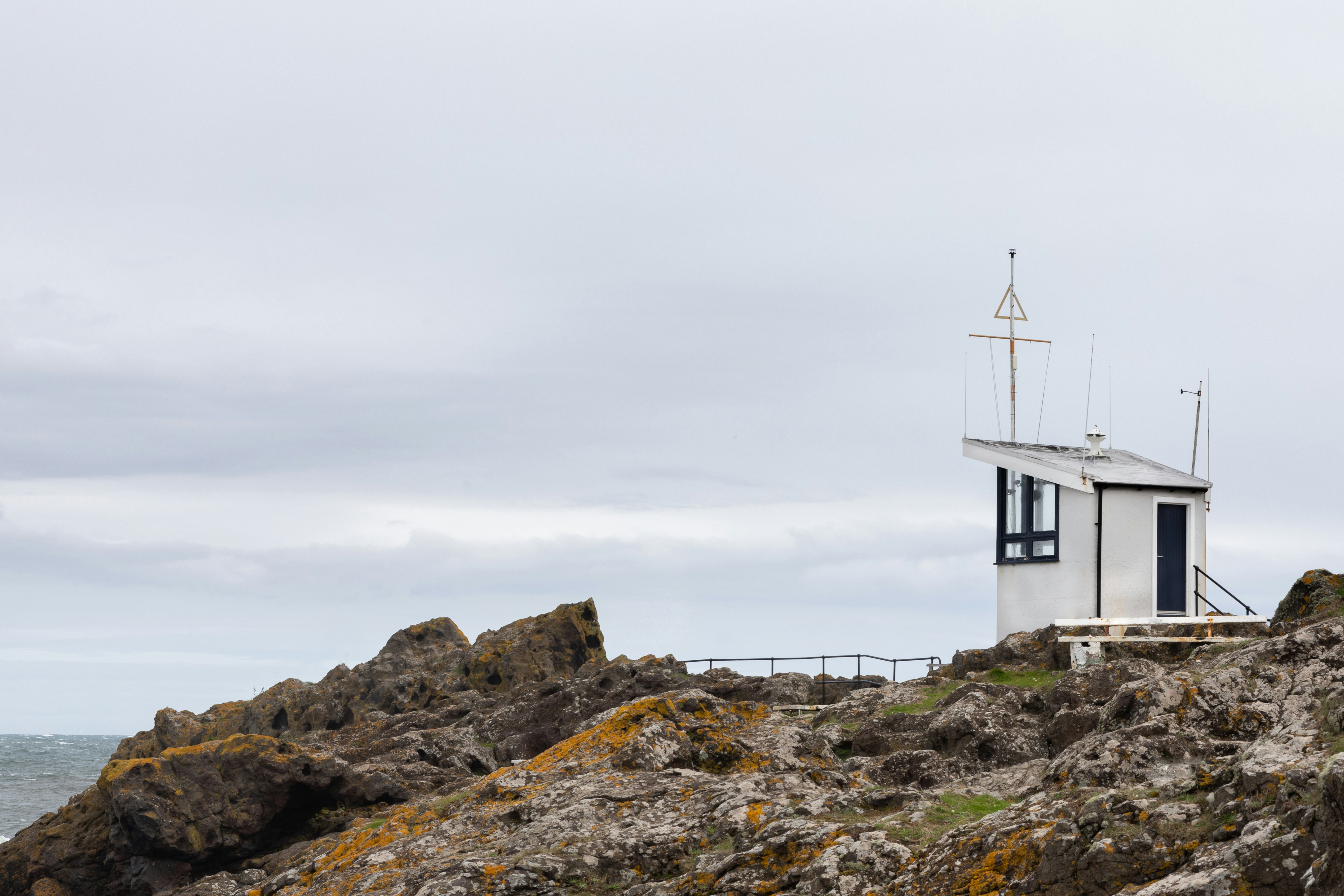 White wooden tower perched on rocky coastline under an overcast sky.
