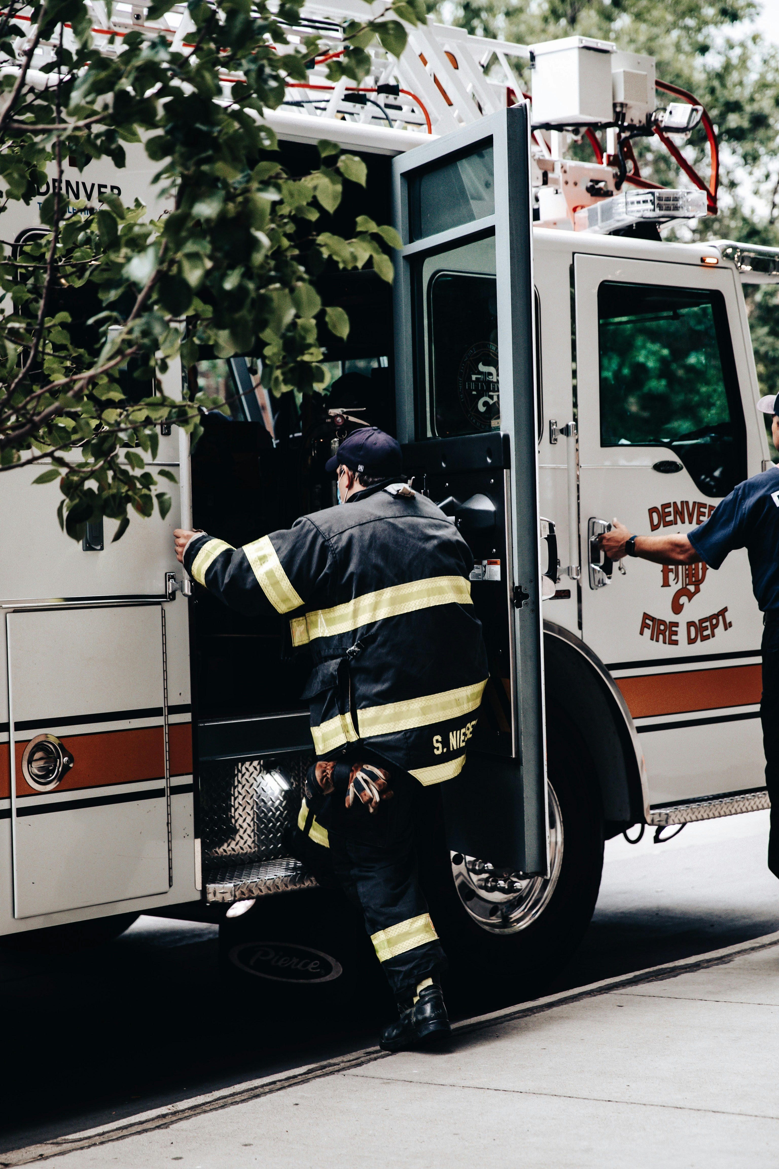 Firefighter entering a fire truck, ready for action, surrounded by urban greenery.