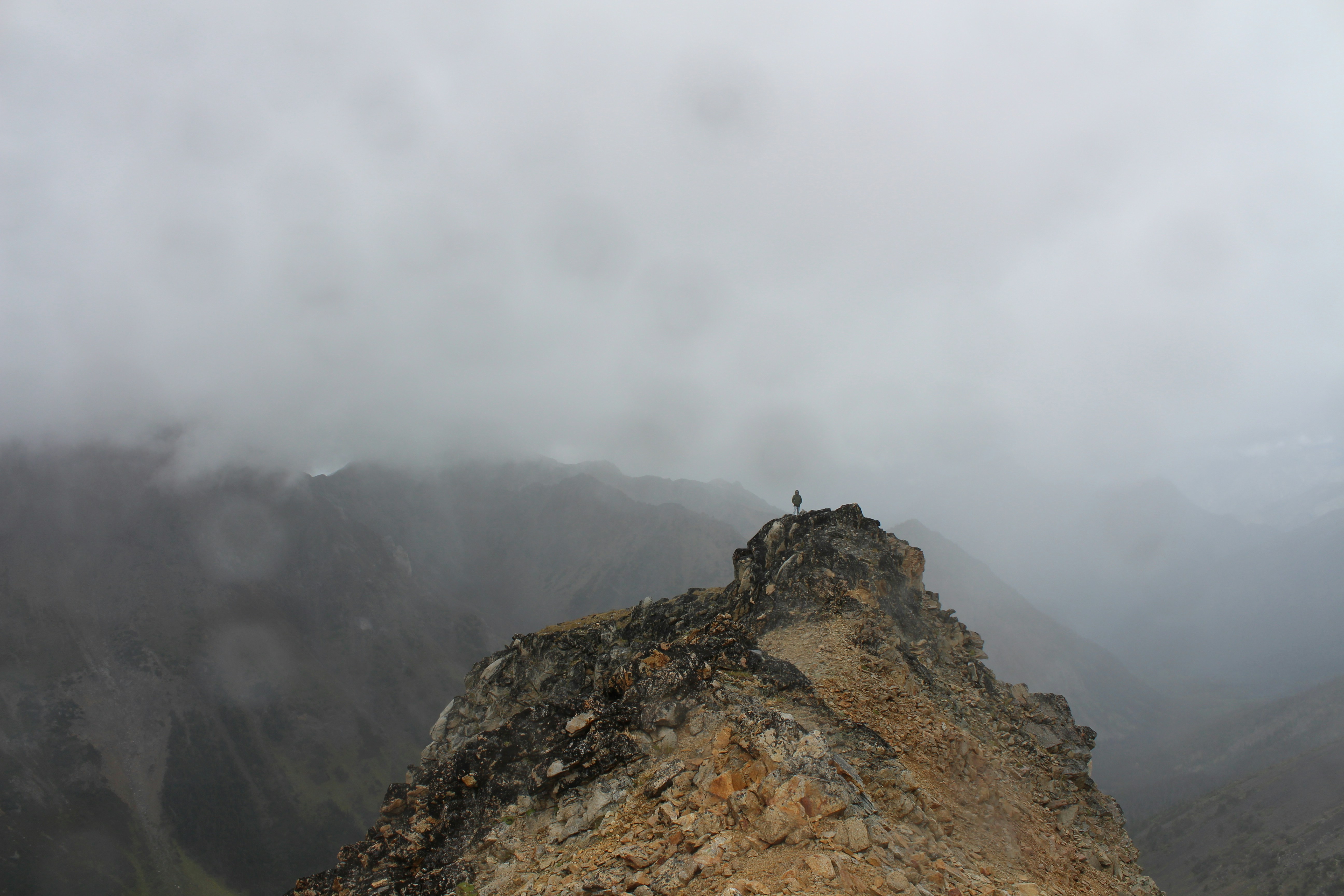 Rugged mountain ridge enveloped in mist with a lone figure standing at its peak.