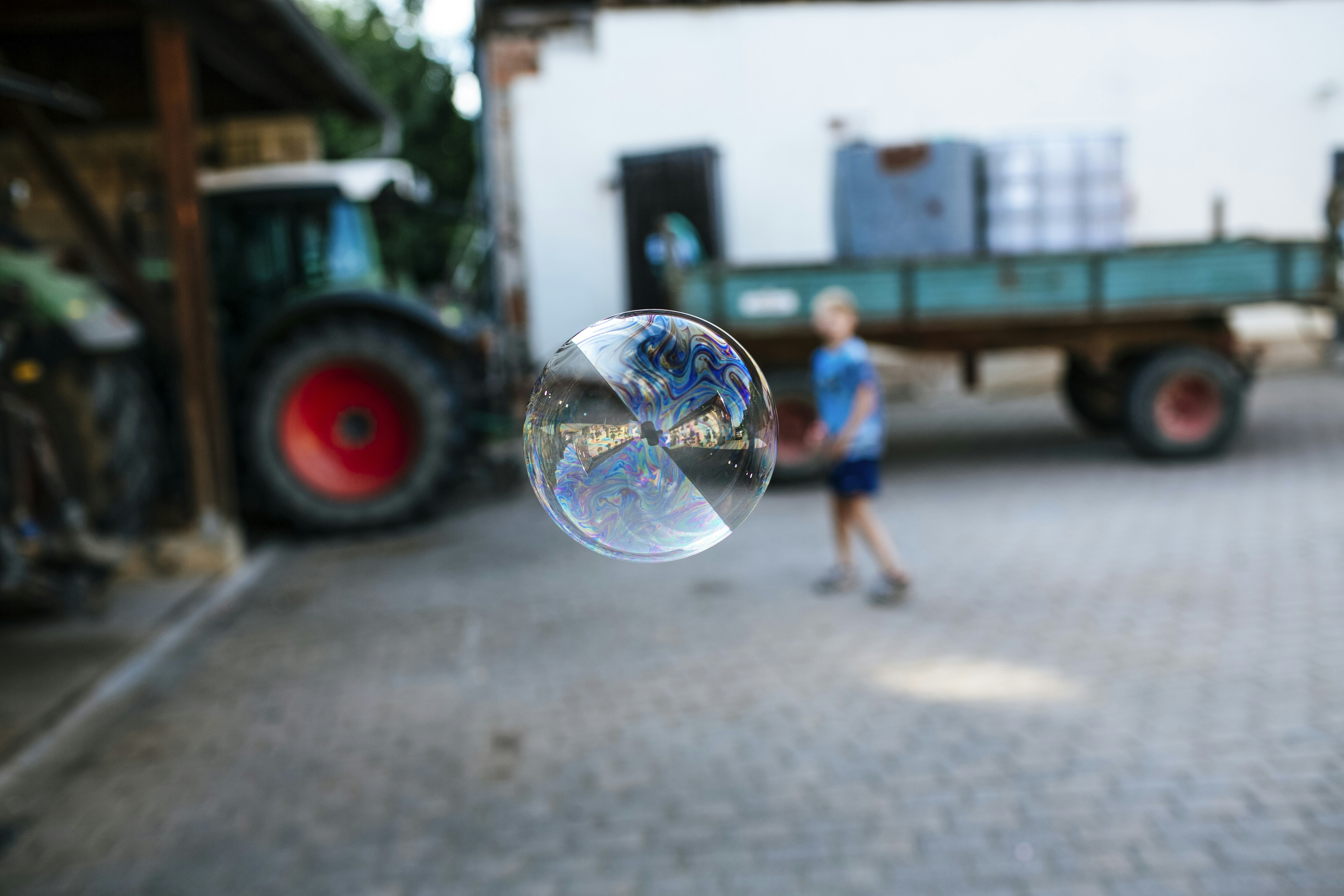 Translucent soap bubble with colorful reflections floating in front of a blurred child and tractor.