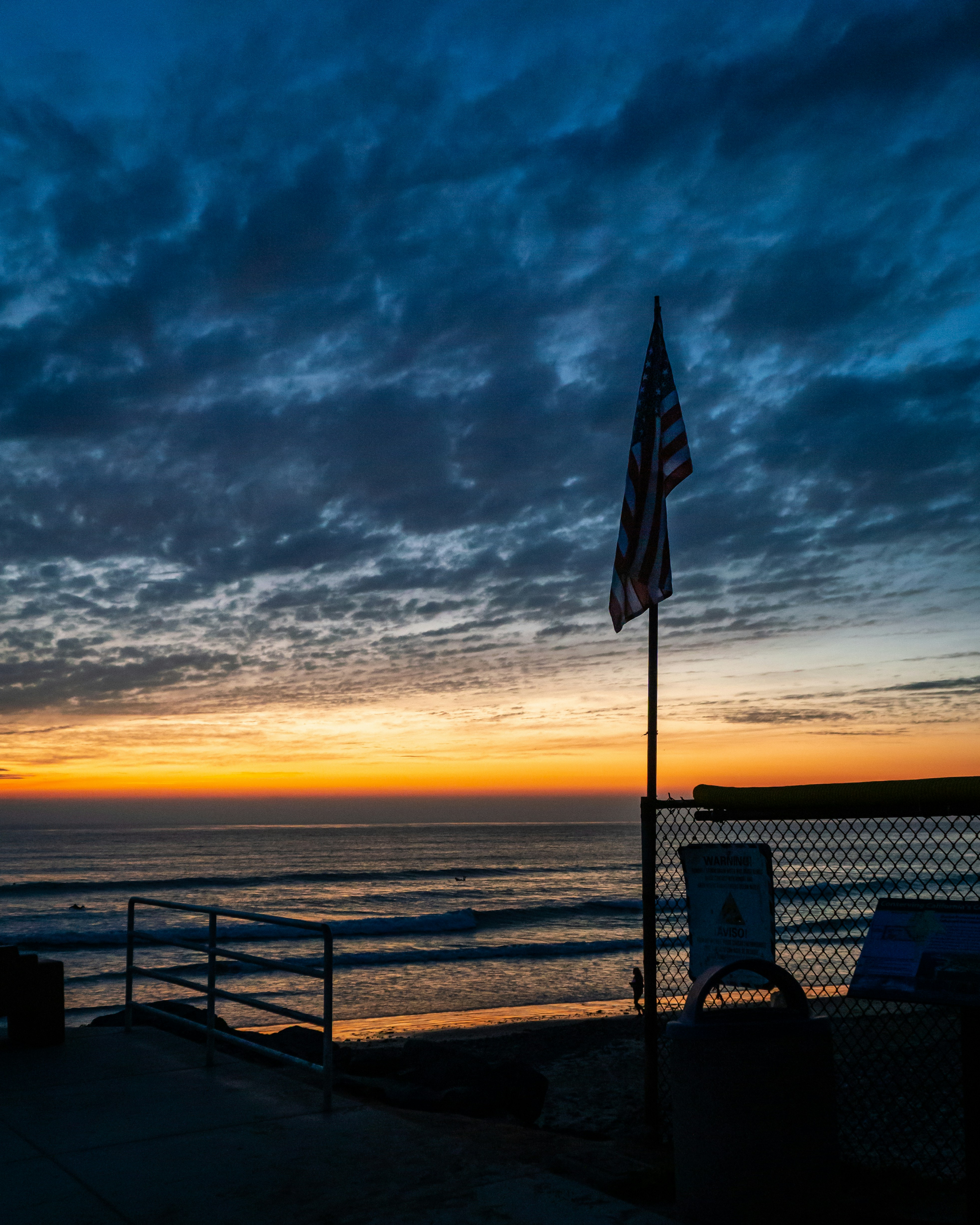 silhouette of flag on pole near body of water during sunset