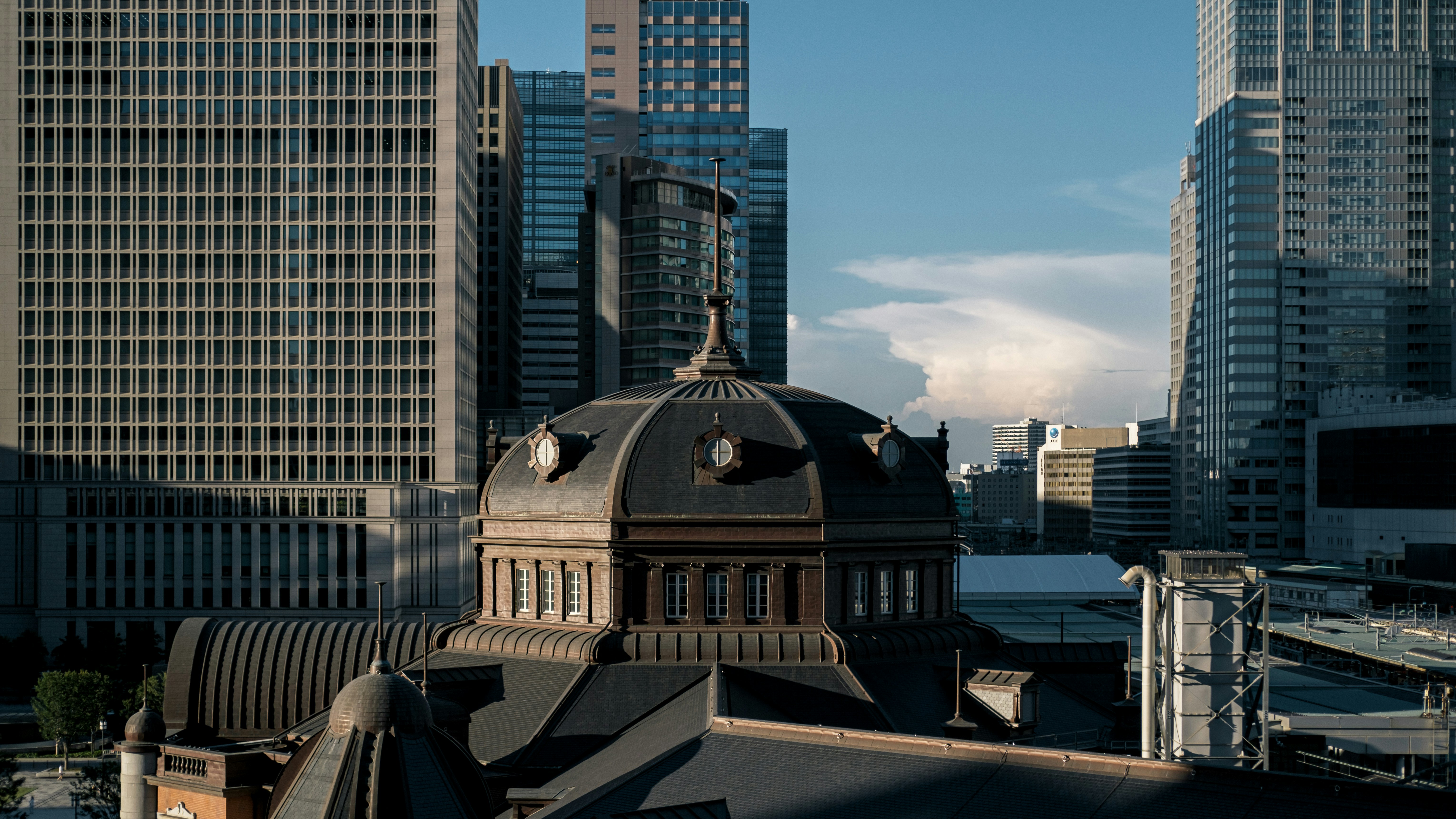 Historic building with a domed roof nestled among towering skyscrapers, showcasing the contrast between architectural styles. 