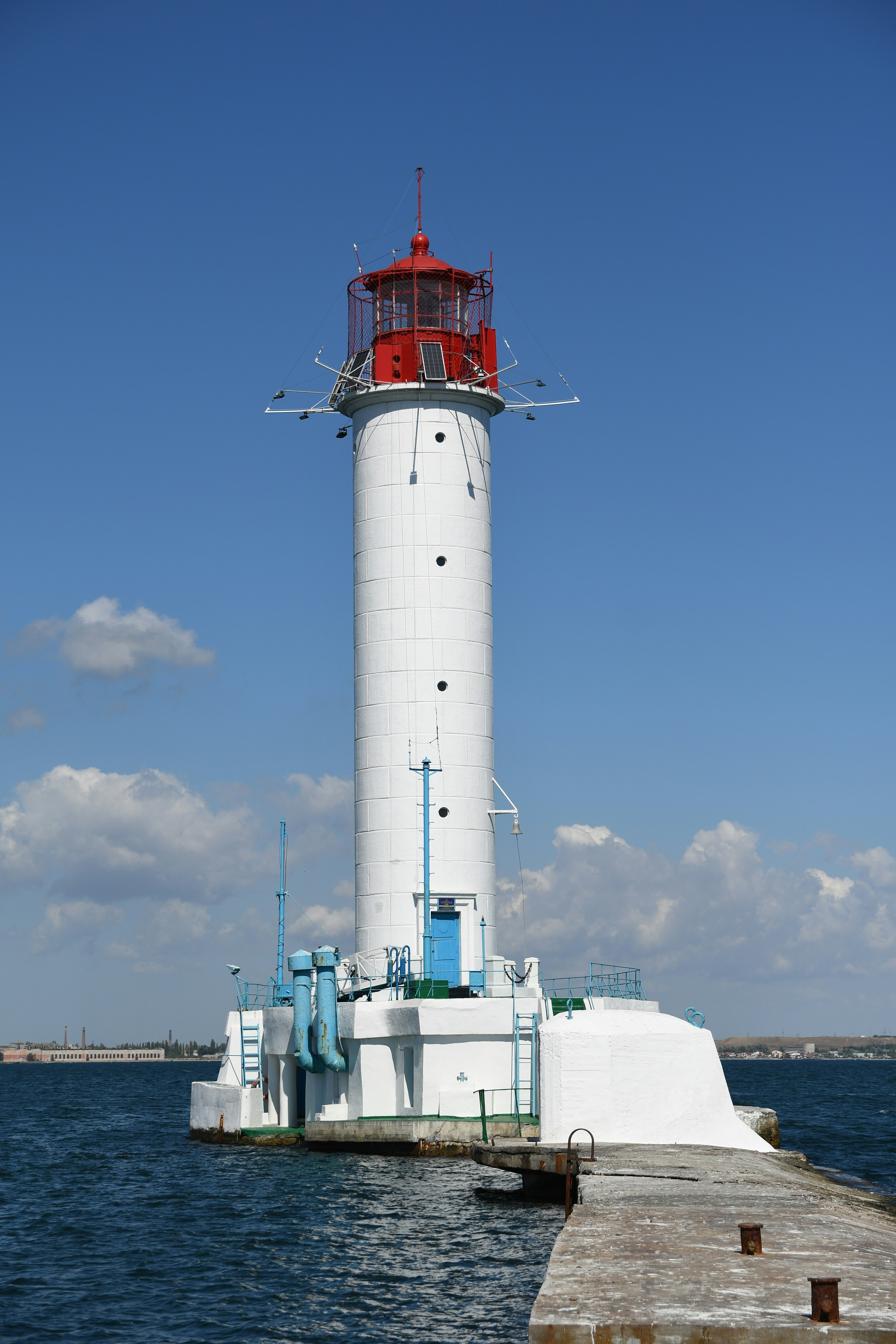 Crimson Crown at the End of the Jetty: A White Lighthouse Over Calm Blue Waters