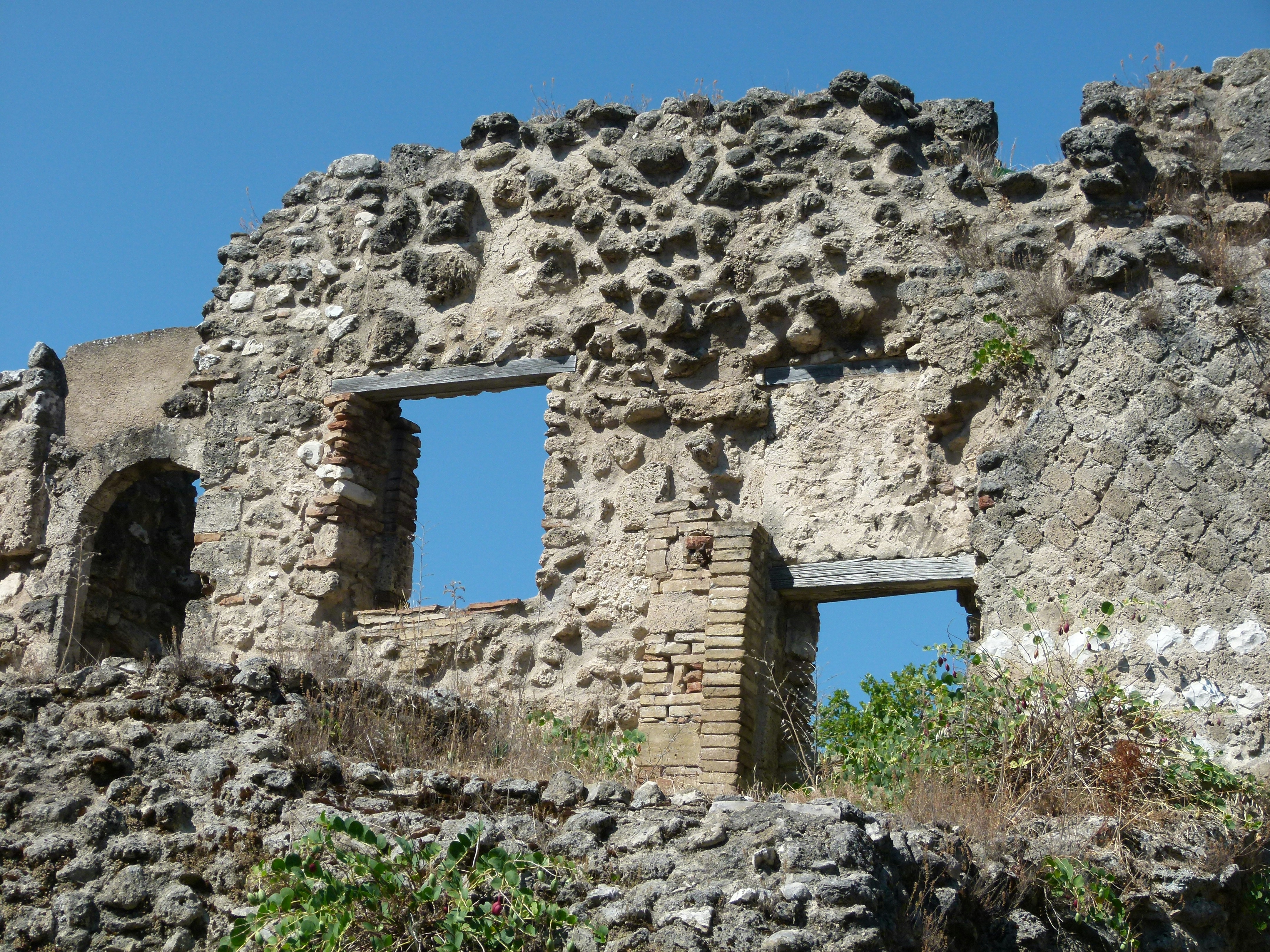 Weathered stone structure with open windows against a clear blue sky.