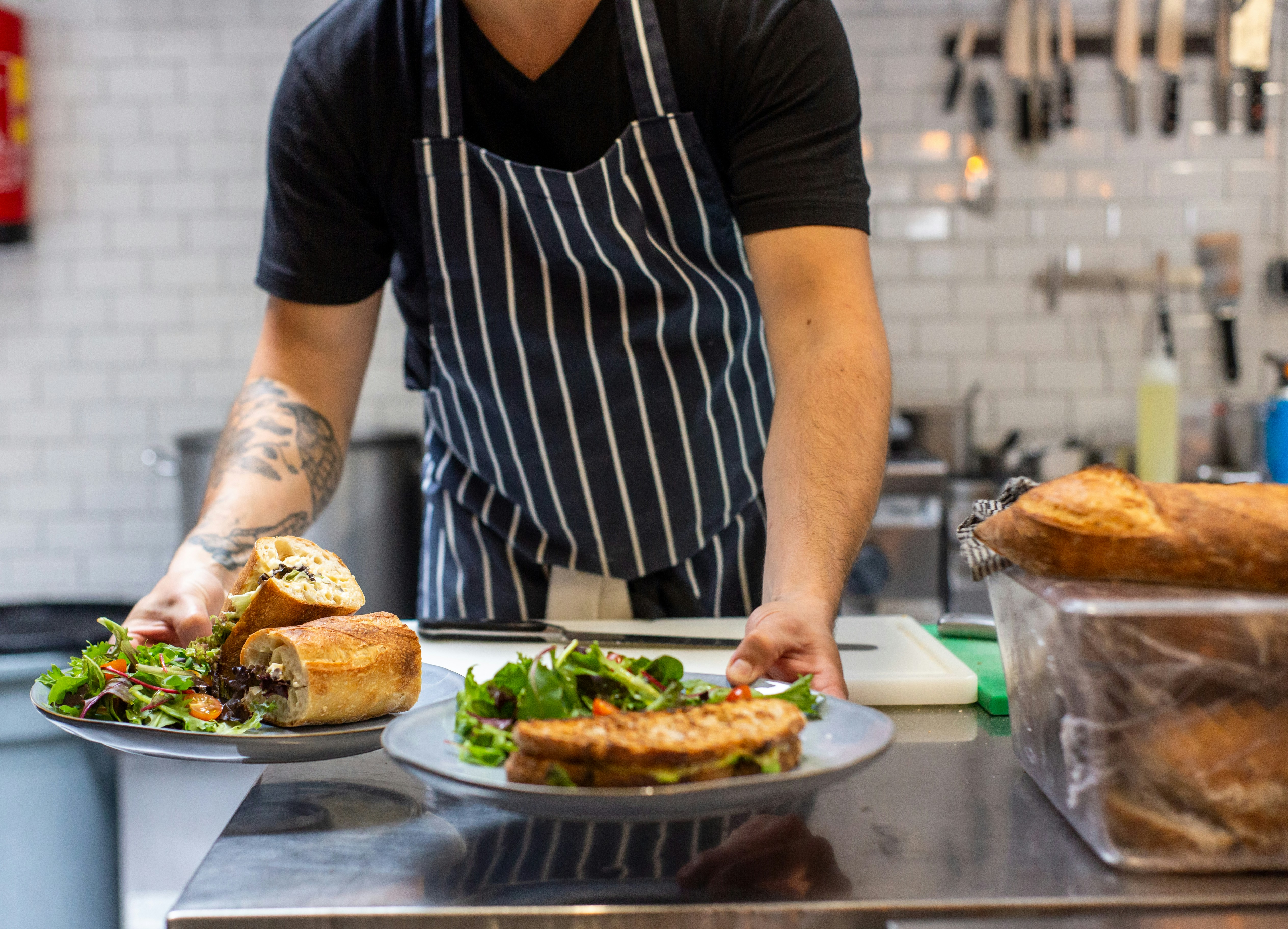 Chef plating gourmet dishes with salads and sandwiches in a professional kitchen.
