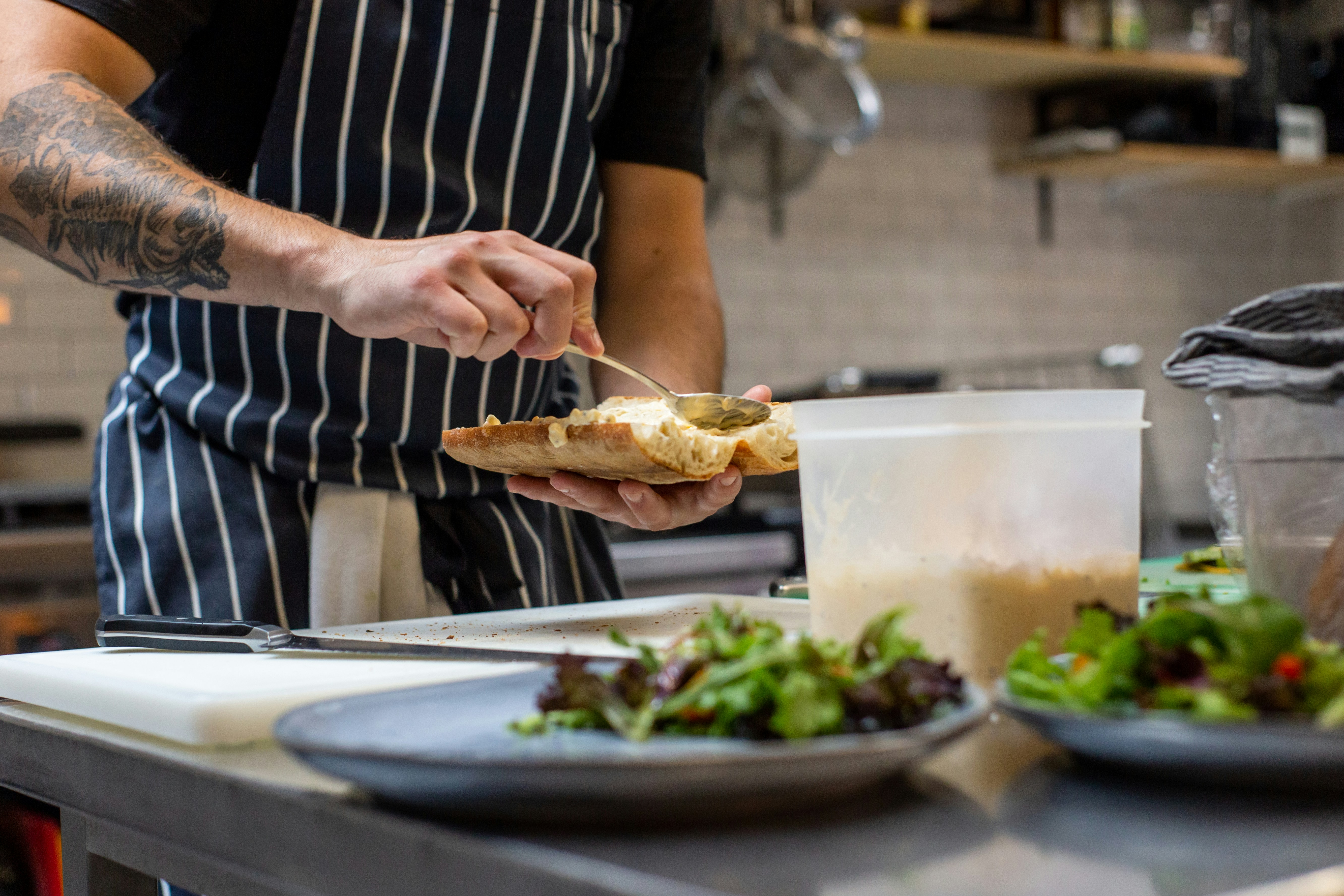 Chef in striped apron preparing a dish with careful attention, surrounded by fresh ingredients in a modern kitchen.