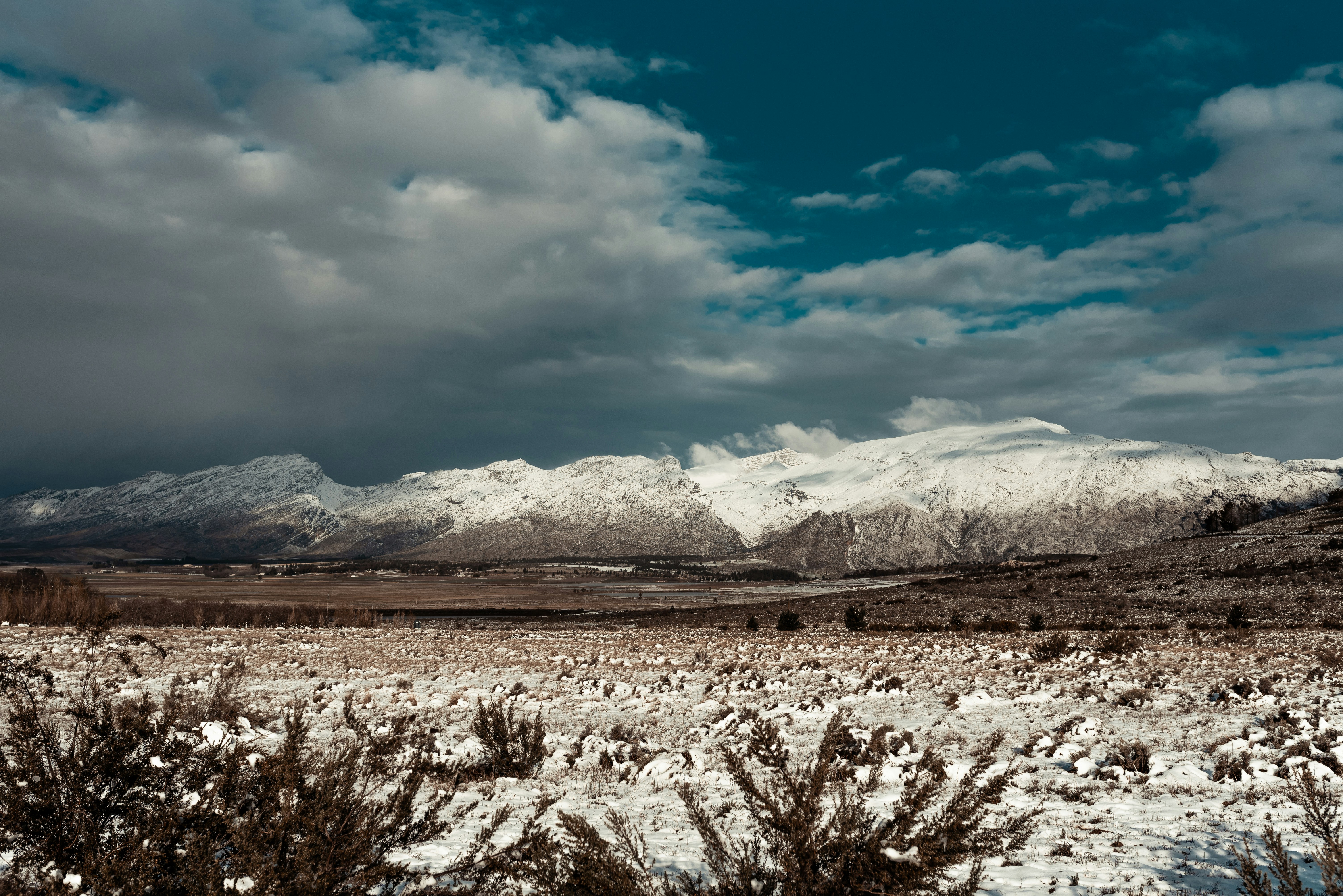 Expansive winter landscape with snow-covered mountains under a dramatic sky, showcasing the stark beauty of nature's chill.