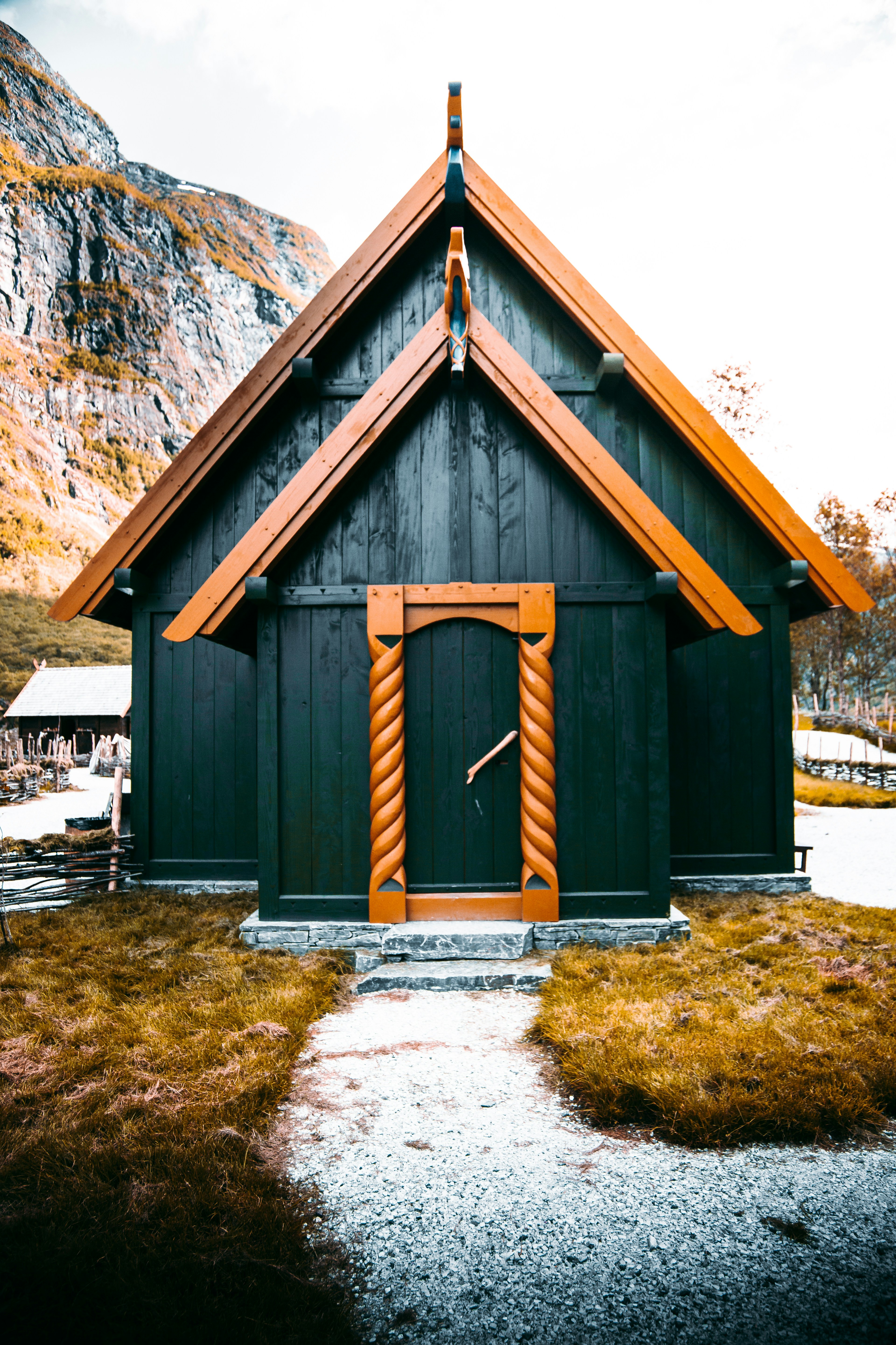 Traditional Nordic-style wooden building with intricate roof design and a distinctive door, set against a backdrop of rocky hills. The structure showcases cultural craftsmanship.