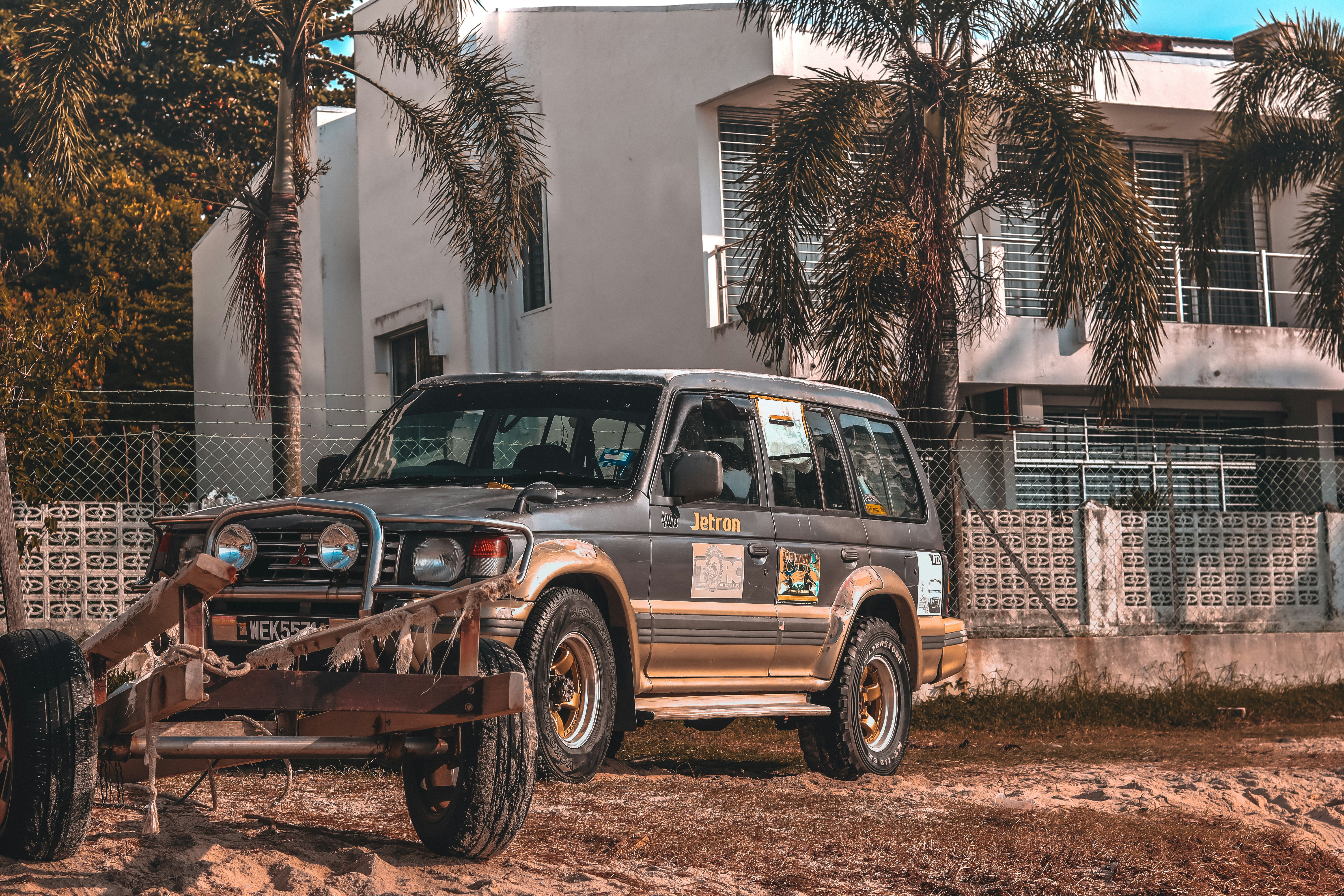 A rugged SUV parked on sandy terrain, surrounded by palm trees and a modern building in the background.