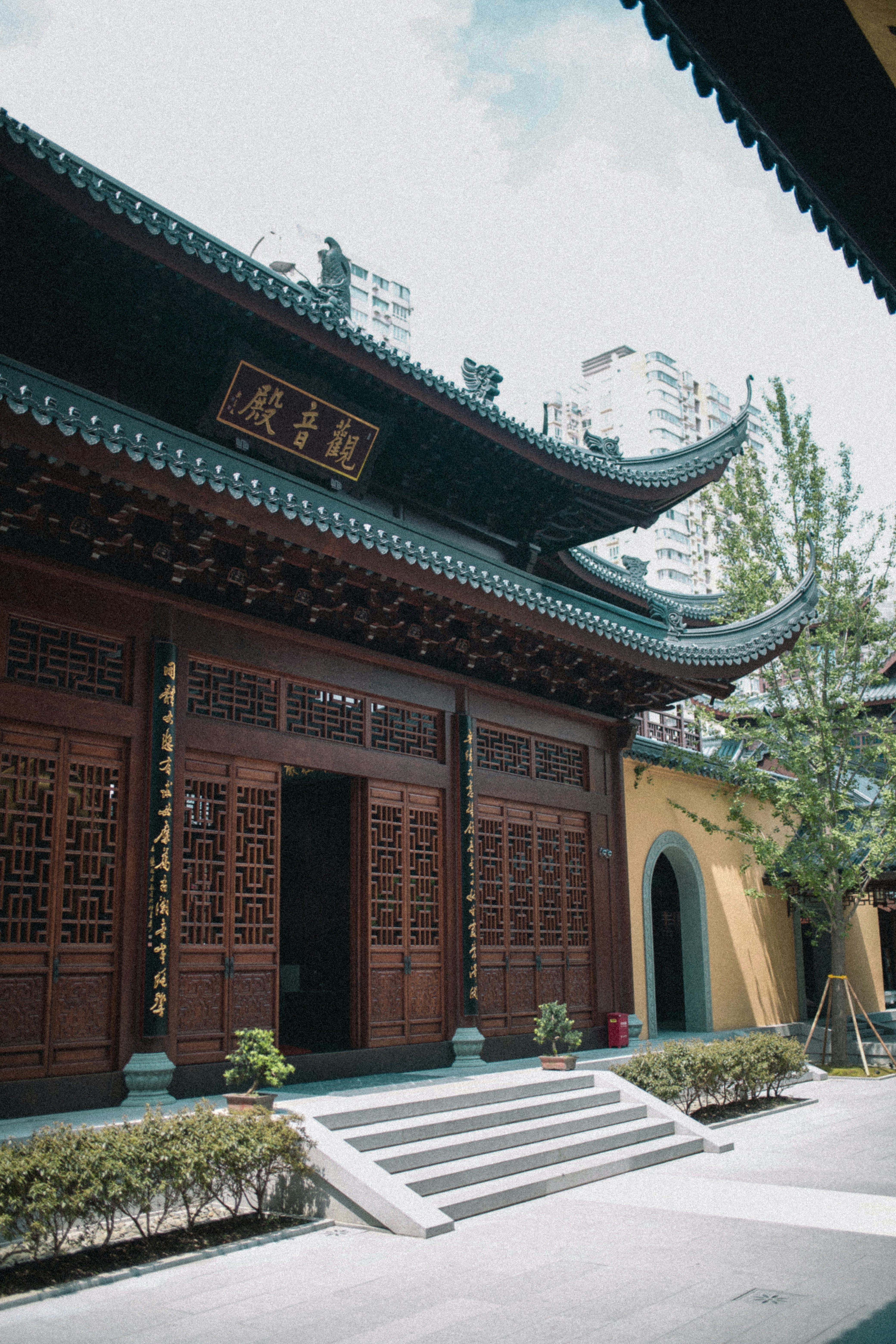 Traditional Chinese architecture featuring intricate wooden details and lush greenery, juxtaposed against a backdrop of modern high-rises.