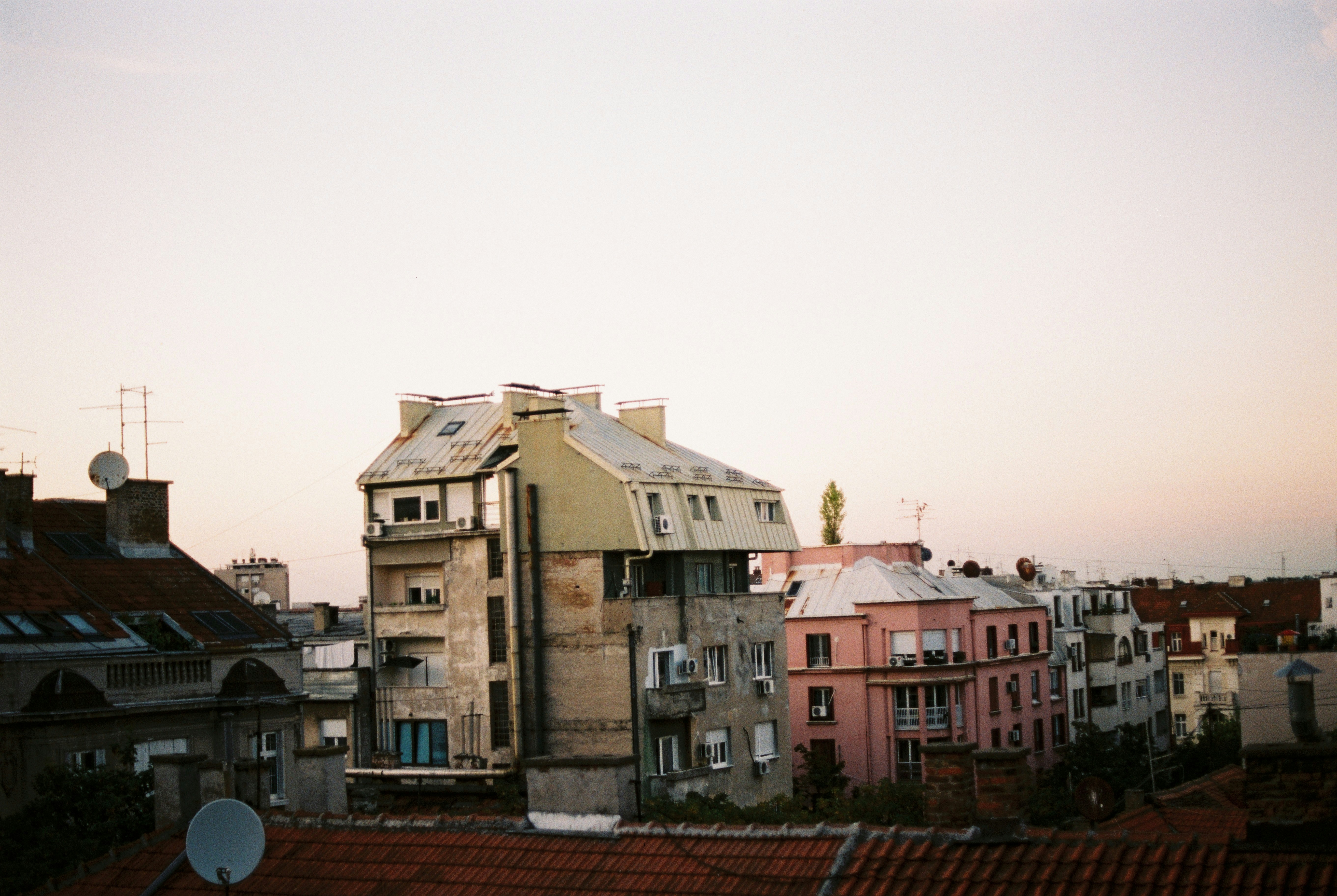 A view of eclectic urban buildings at dusk, showcasing a blend of aged and modern architecture. The soft pastel sky enhances the scene's tranquility.