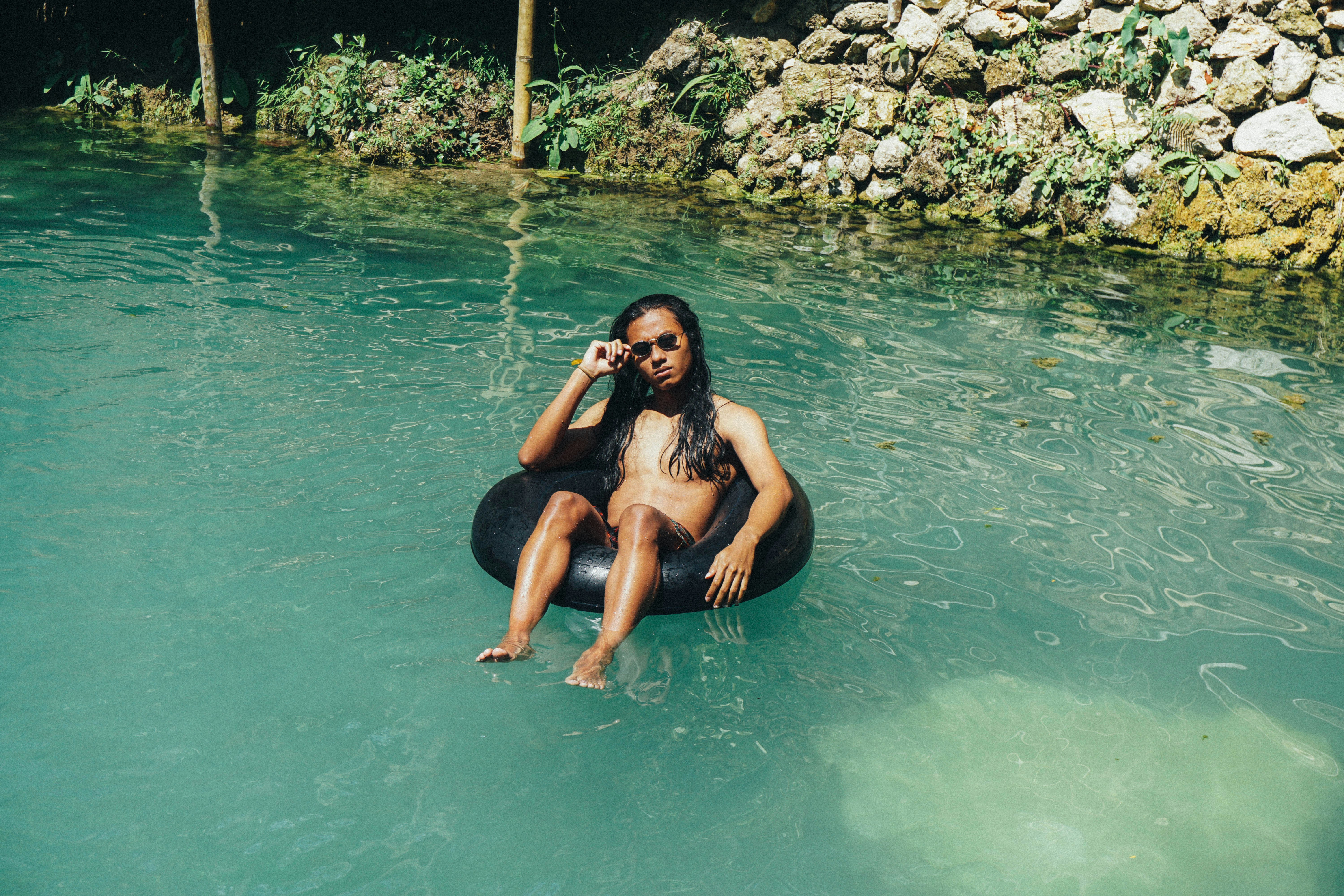 woman in black bikini sitting on rock in water during daytime
