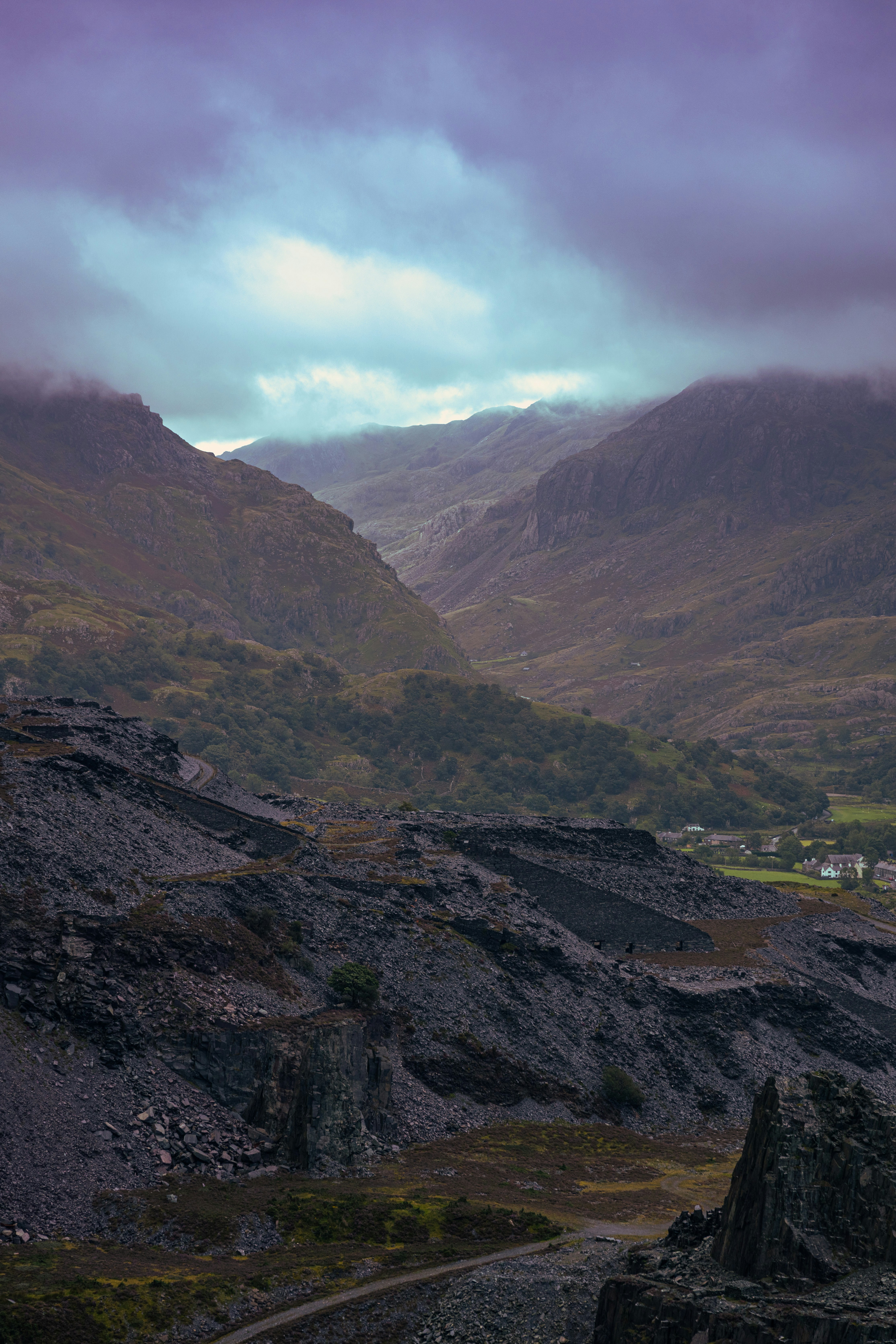 Dramatic view of rugged mountains and slate quarries under a moody sky, highlighting the remnants of industrial activity in a serene landscape.