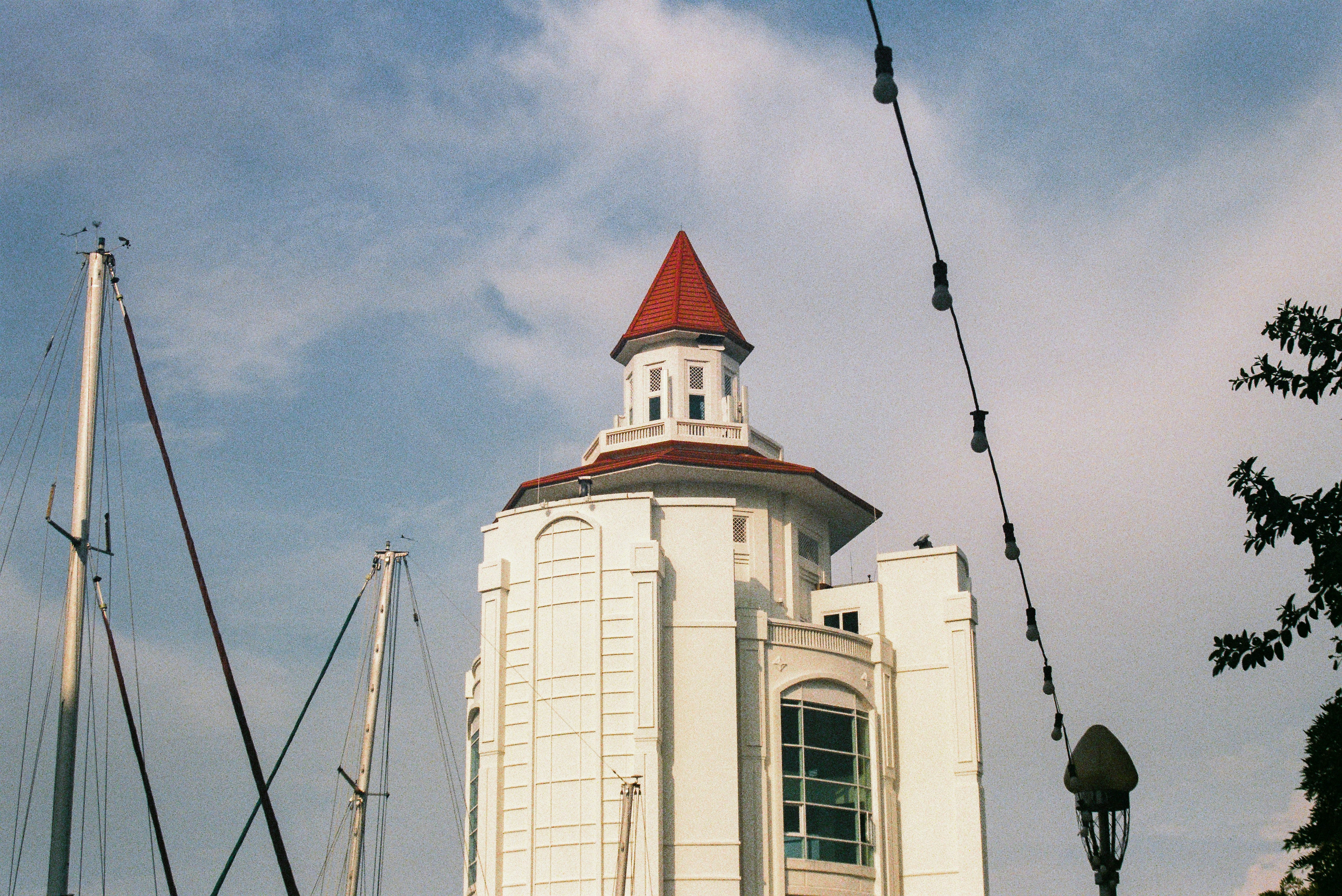 White Turreted Harbor Tower Framed by Sail Masts and Festooned Lights